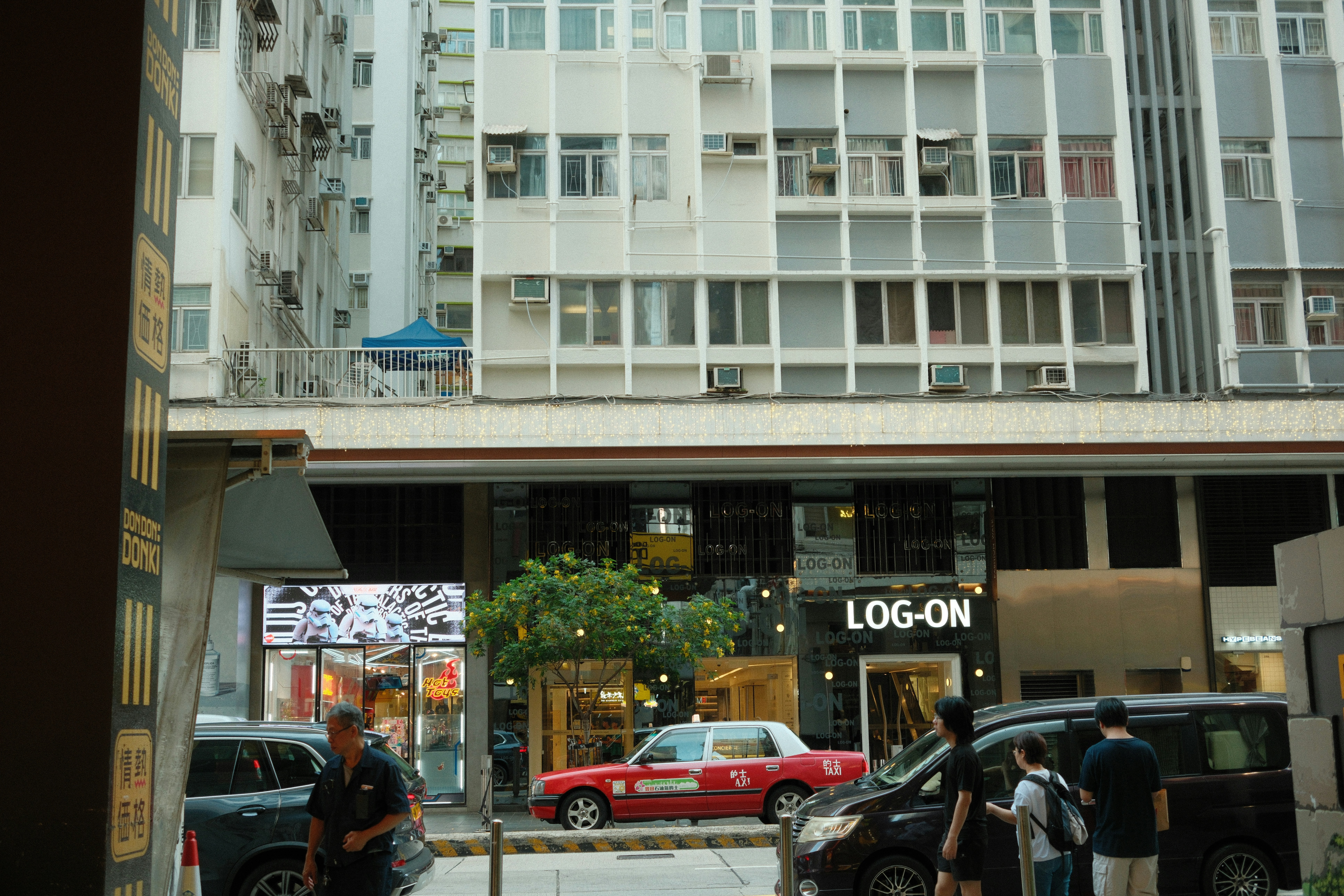 A vibrant street scene showcasing a mix of vehicles and pedestrians in an urban setting, with a prominent store front displaying 'LOG-ON'.