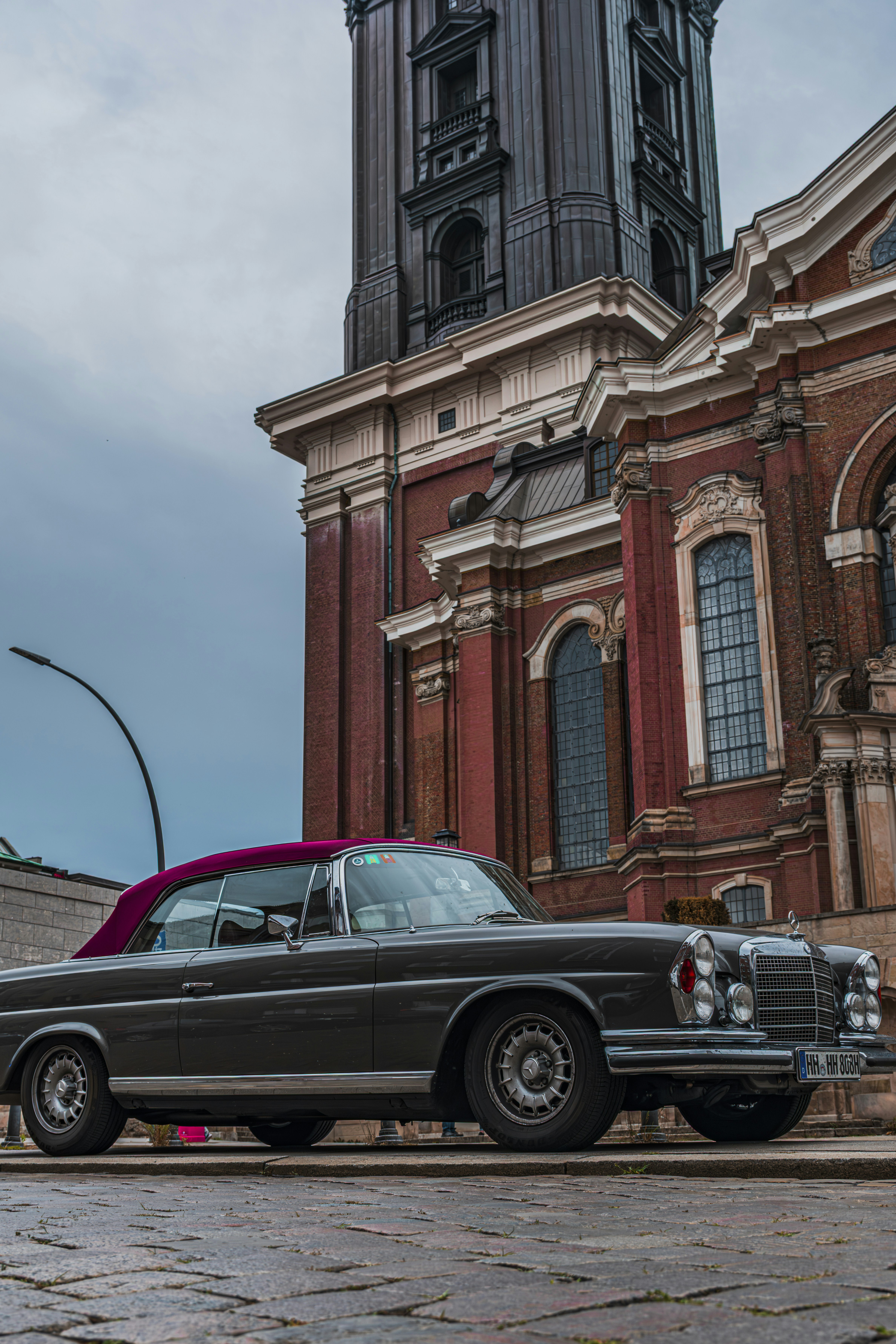 Classic convertible parked beside a historic building, showcasing a blend of vintage automotive design and architectural beauty.