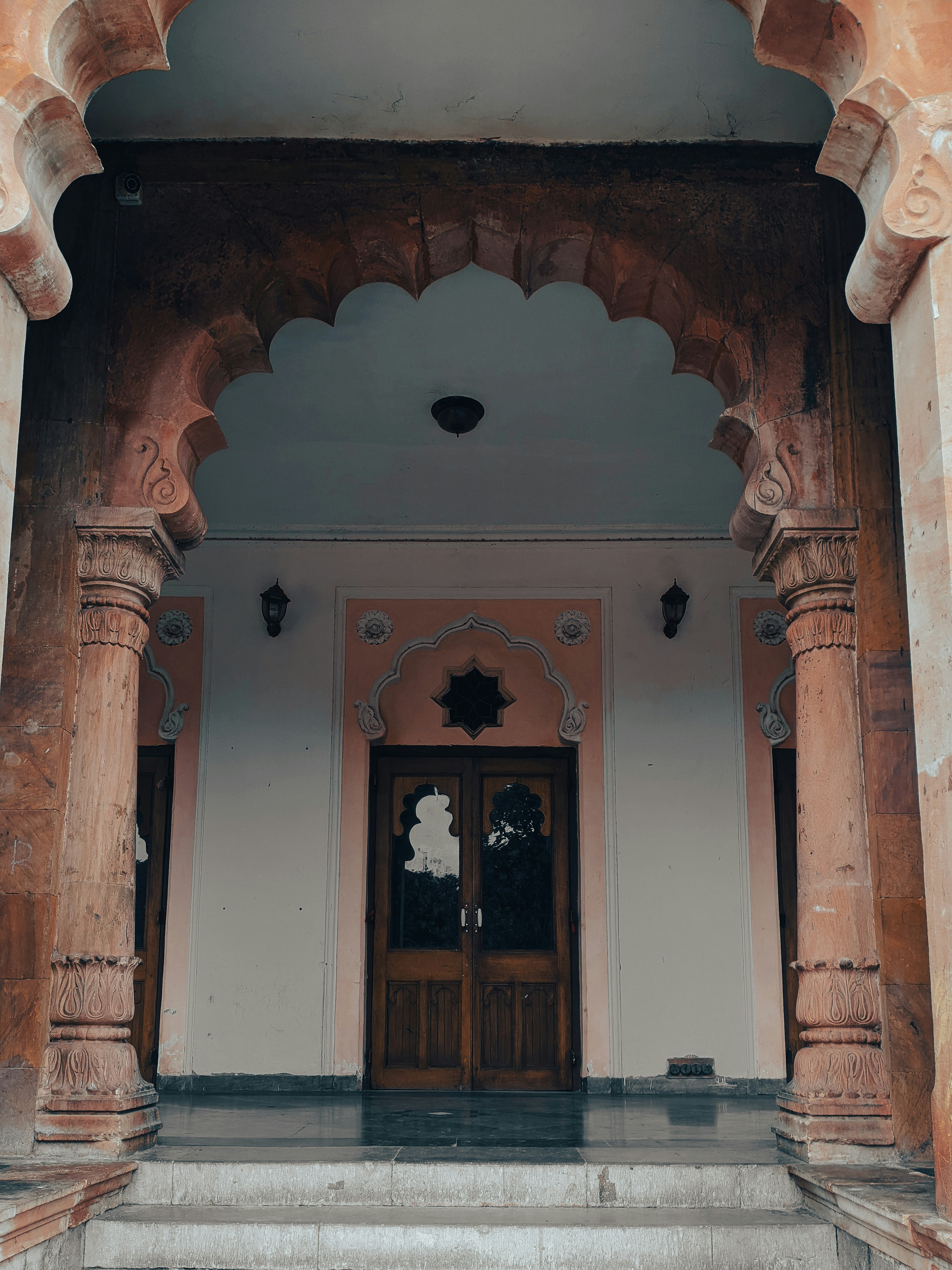 A minimalistic door of Gandhi Hall, showcasing simple yet elegant architectural design. | A detailed archway frames the wooden double doors.