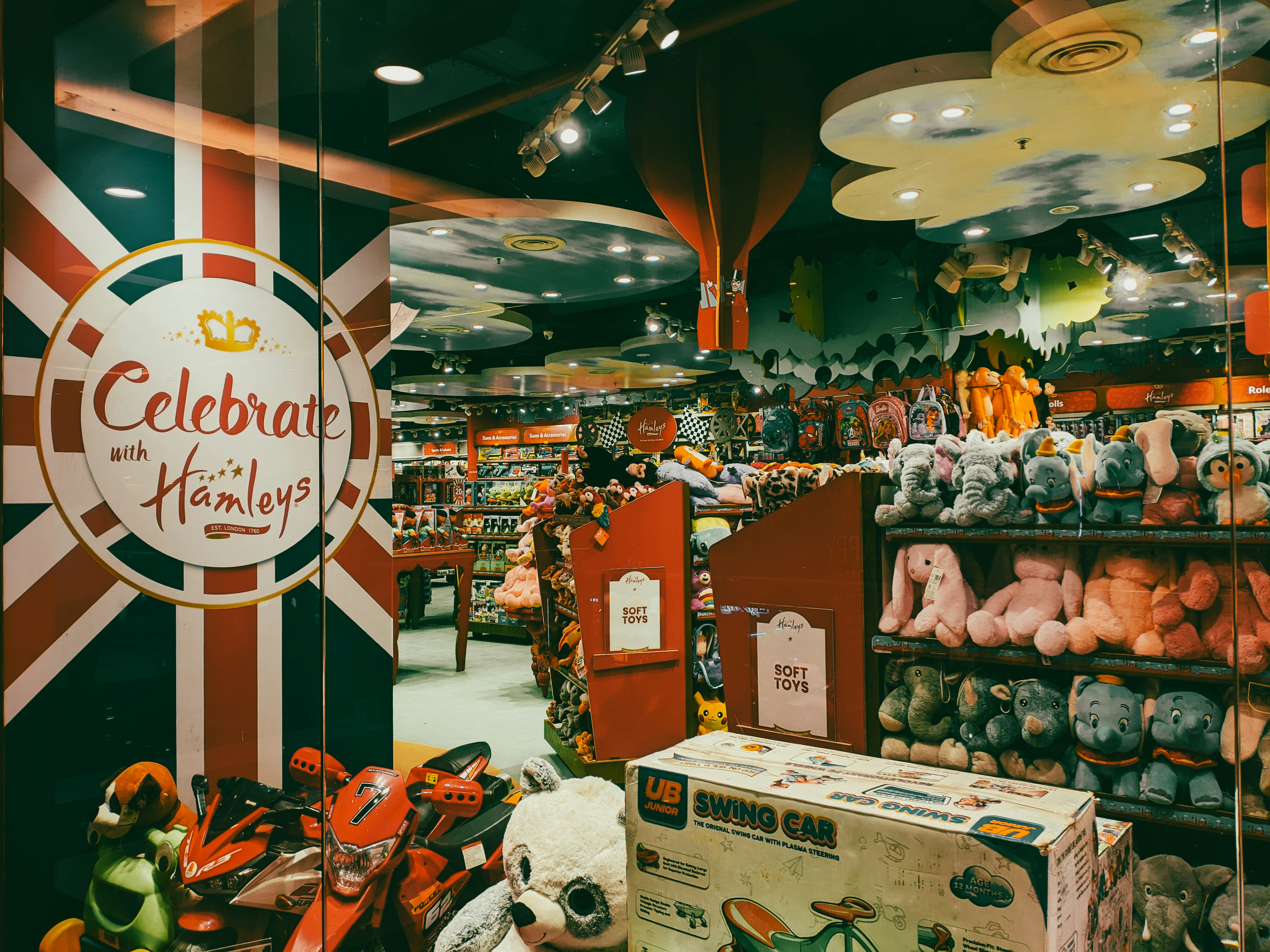 Toy store exterior with colorful window displays and playful decorations. | A toy store, hamleys, with many shelves of toys.