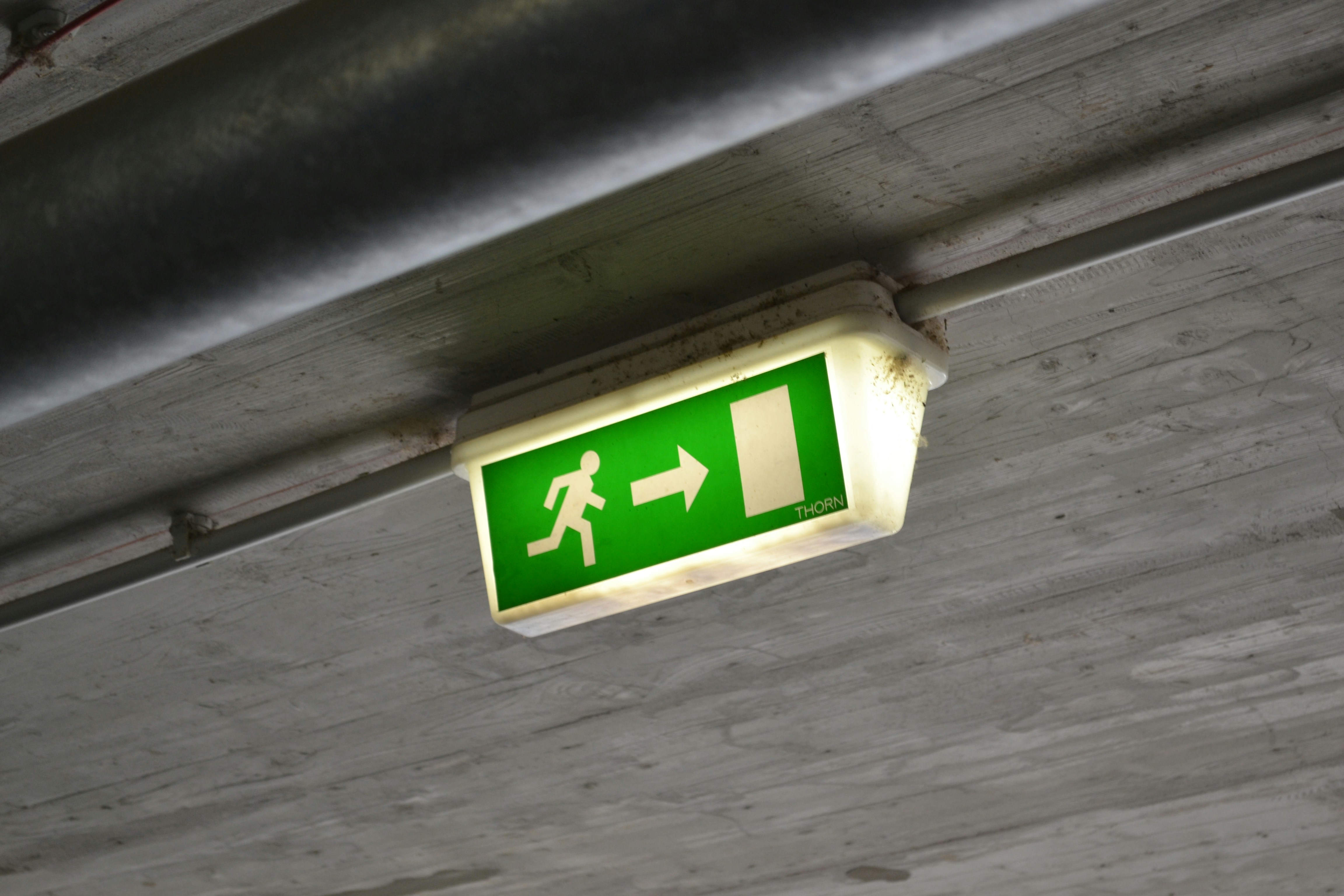 Emergency exit sign illuminating a concrete ceiling in a parking structure, directing towards an exit.