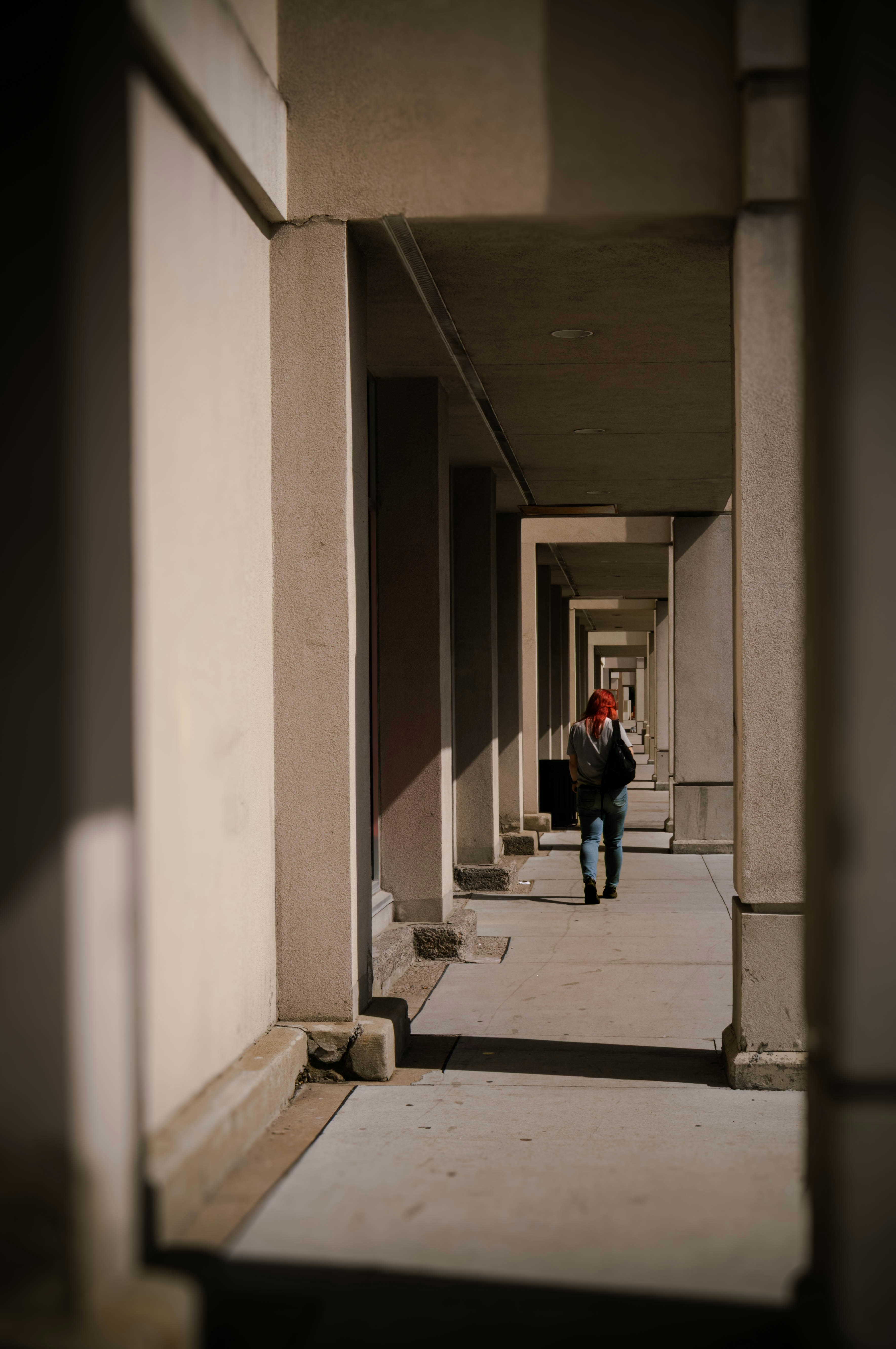 Urban perspective with repeating columns and a solitary figure walking away. | A person walks through an architectural corridor.