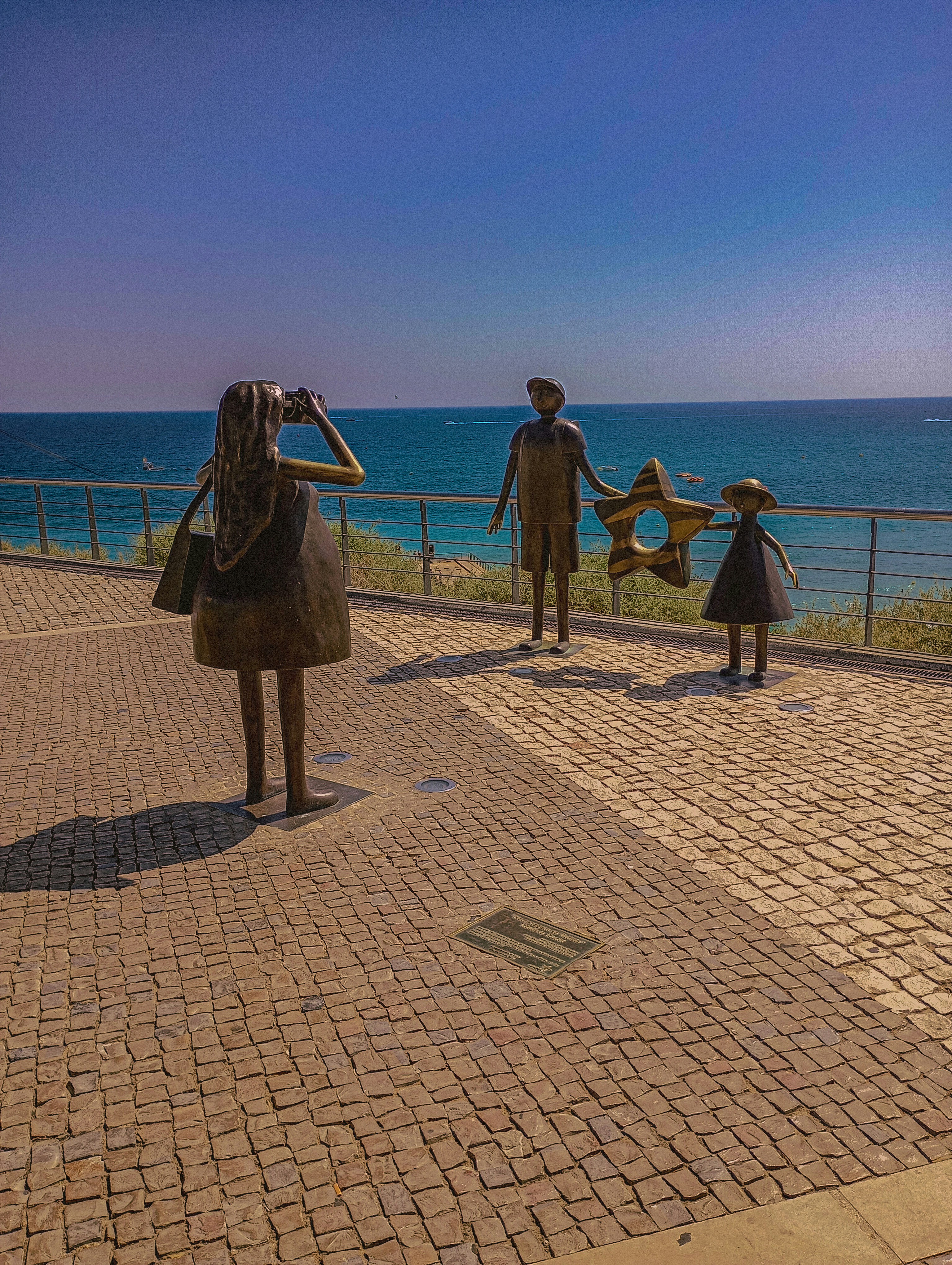 Echoes by the Sea: Bronze Figures on a Cobblestone Promenade