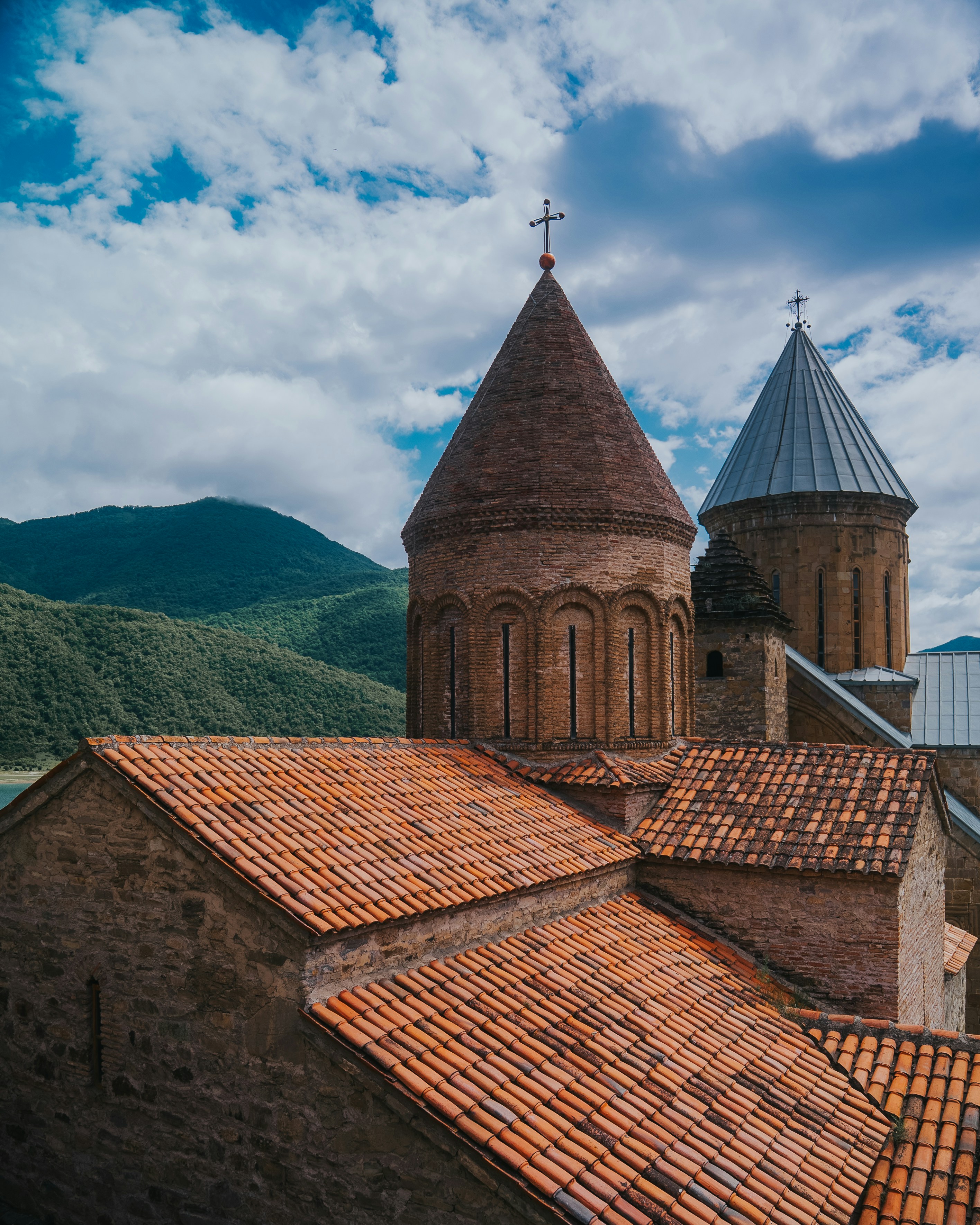 Two historic church towers rise against a backdrop of rolling hills and clouds, showcasing intricate architectural details and terracotta roofs.