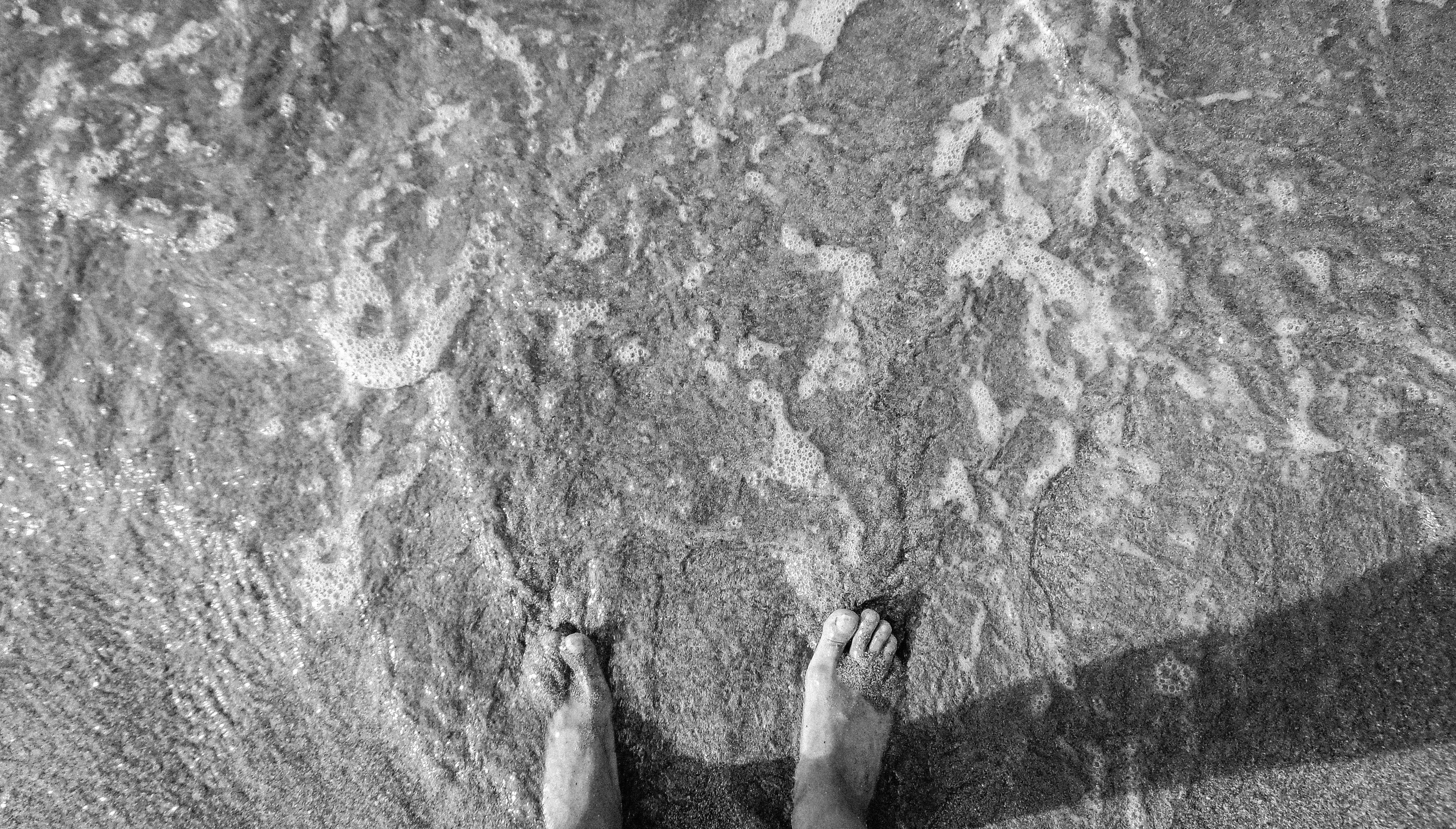 Bare feet touching gentle waves on a sandy beach, capturing a moment of tranquility and connection with nature.