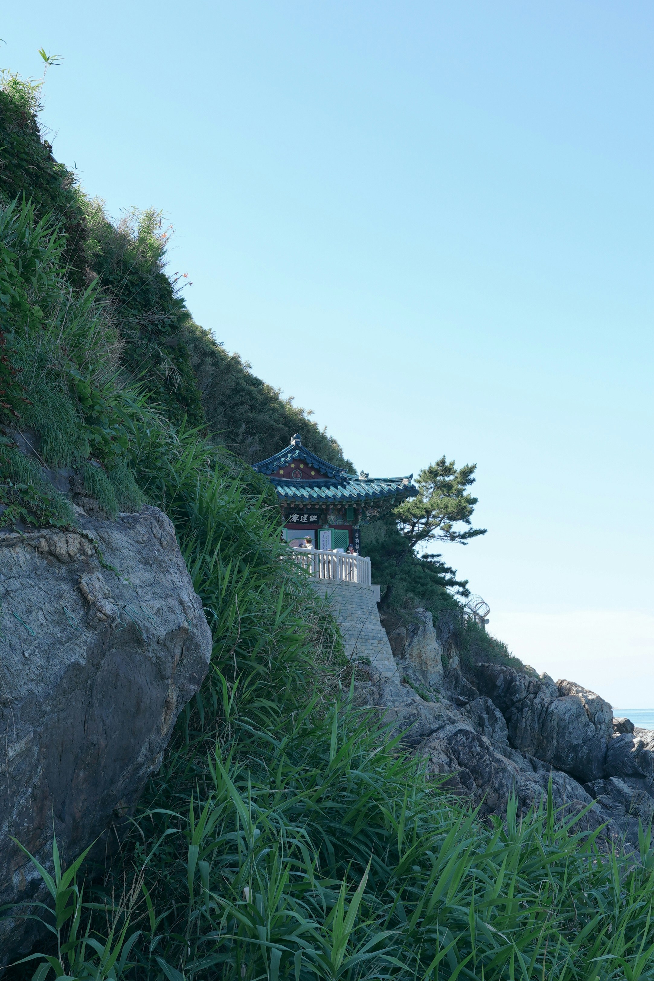 Traditional architecture perched on a rocky coastline, surrounded by lush greenery and overlooking the ocean.