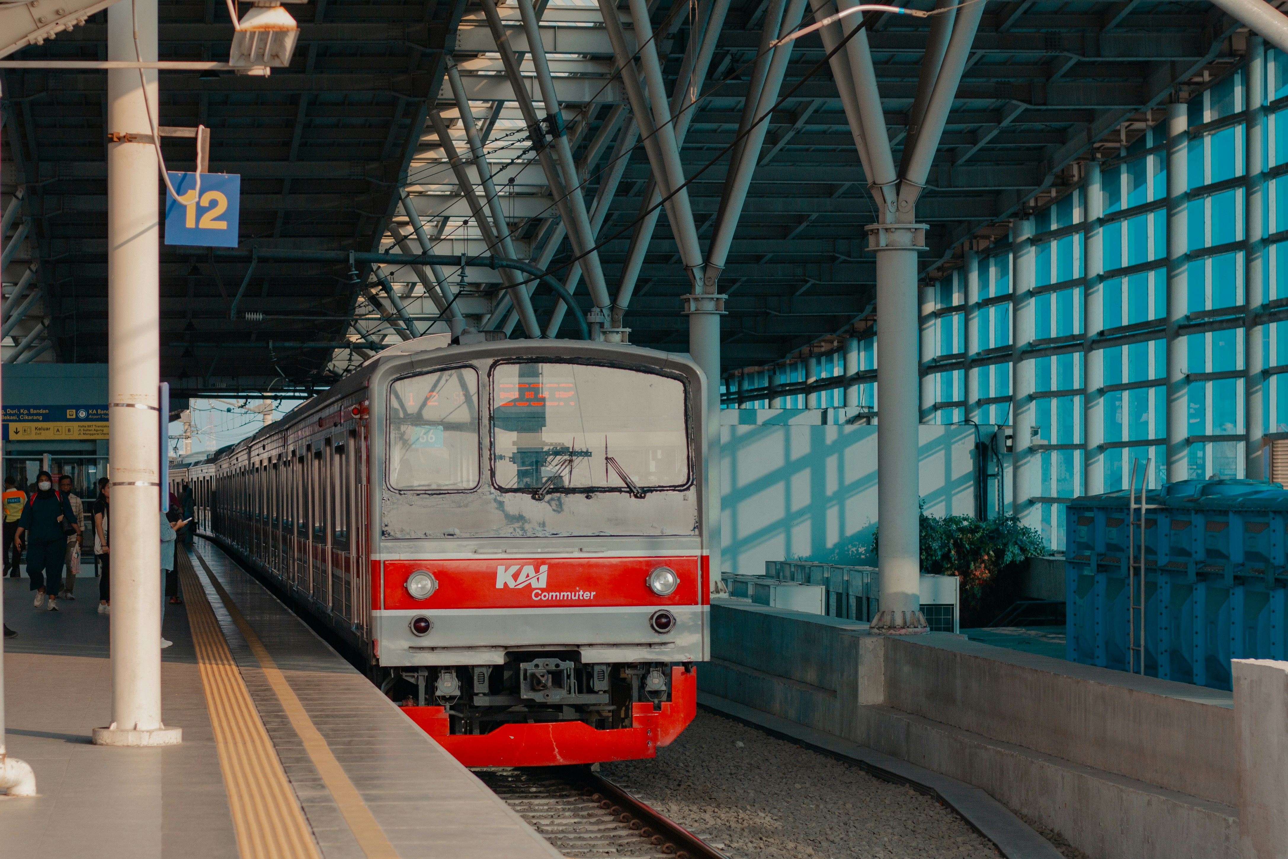 KAI commuter train arriving at a modern station, showcasing sleek design and vibrant colors against a backdrop of architectural lines and shadows.