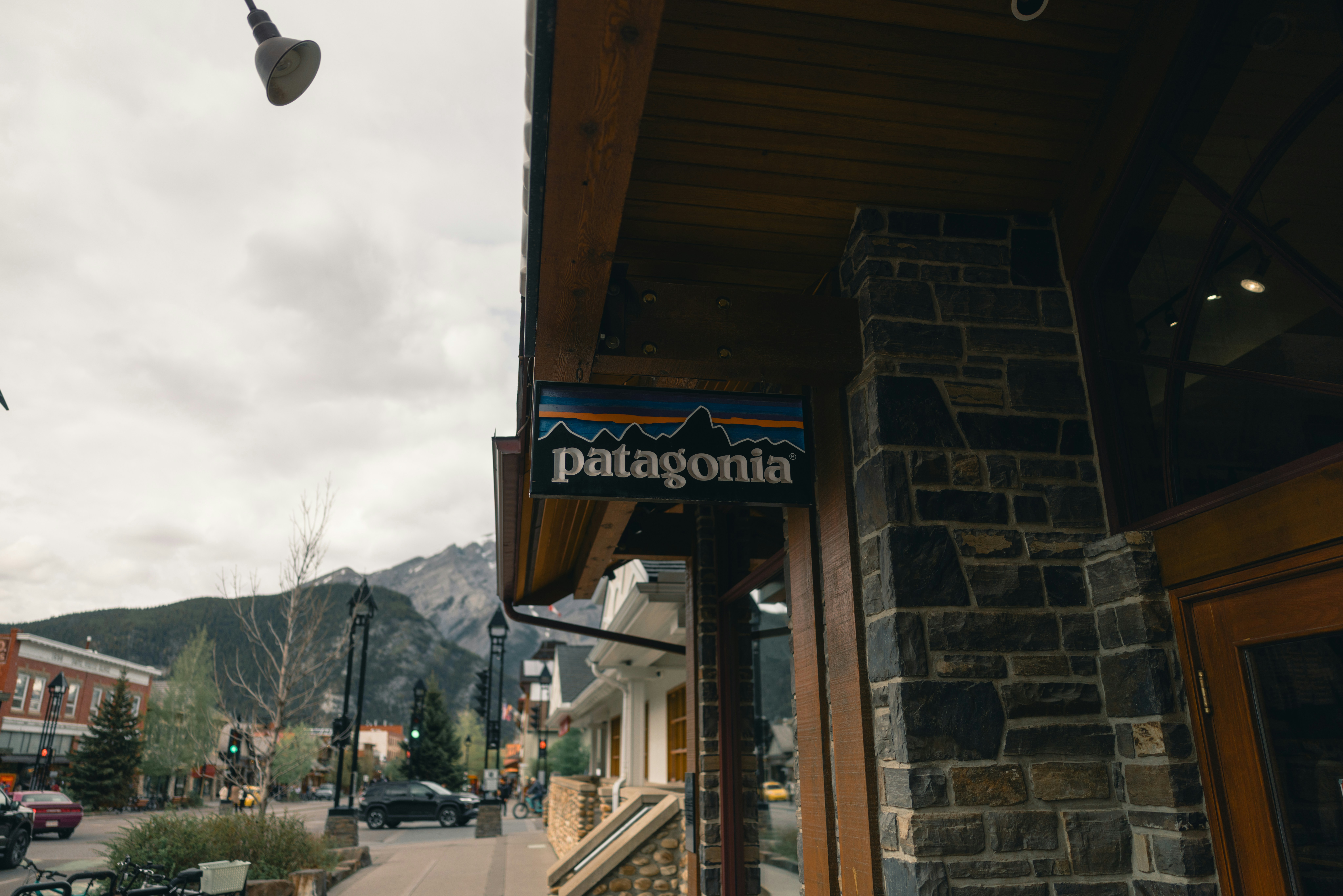 Patagonia storefront under a cloudy sky, showcasing the brand's logo with a backdrop of rugged mountains. The scene highlights the connection between outdoor adventure and retail.