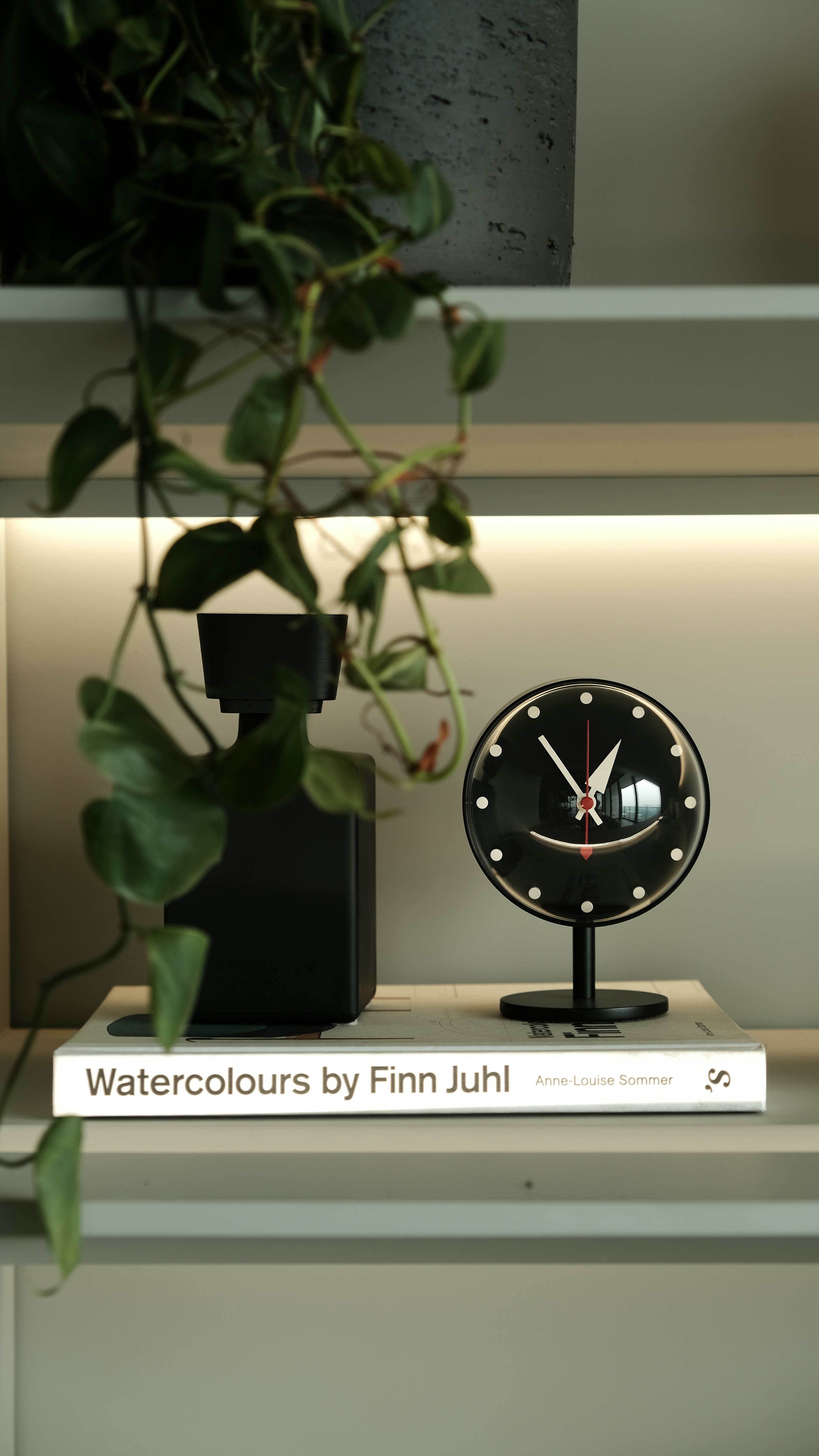 Mid-Century Desk Clock resting on a book under a trailing plant