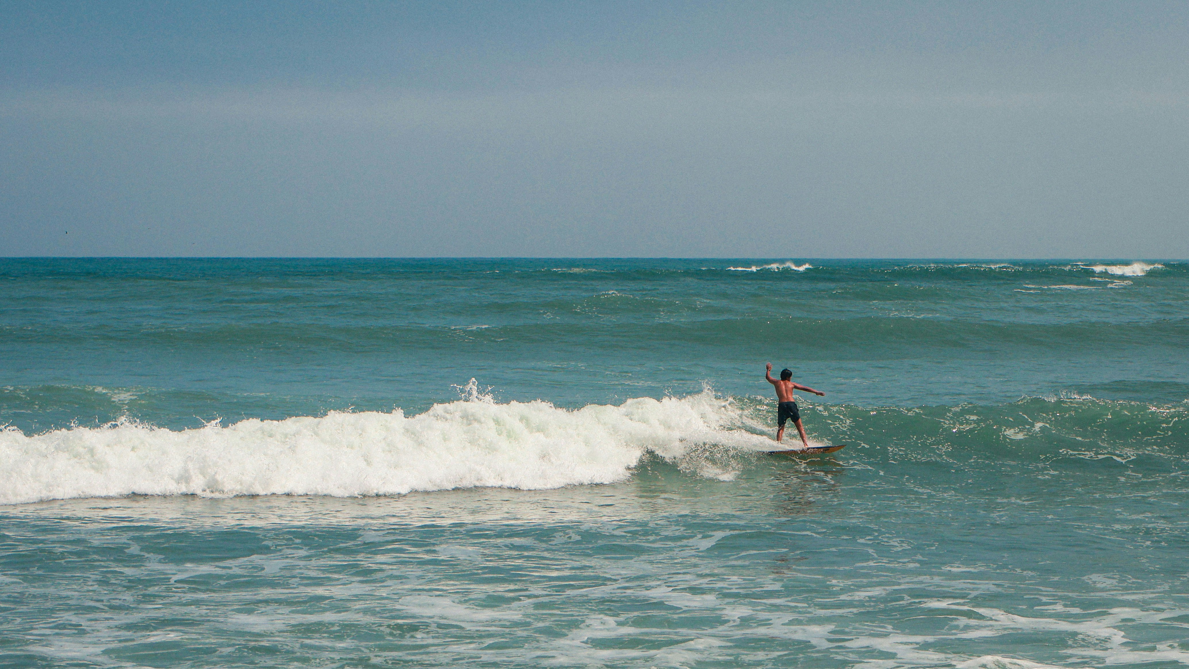 Surfer skillfully maneuvering on a wave under a clear sky, showcasing the thrill of ocean sports.