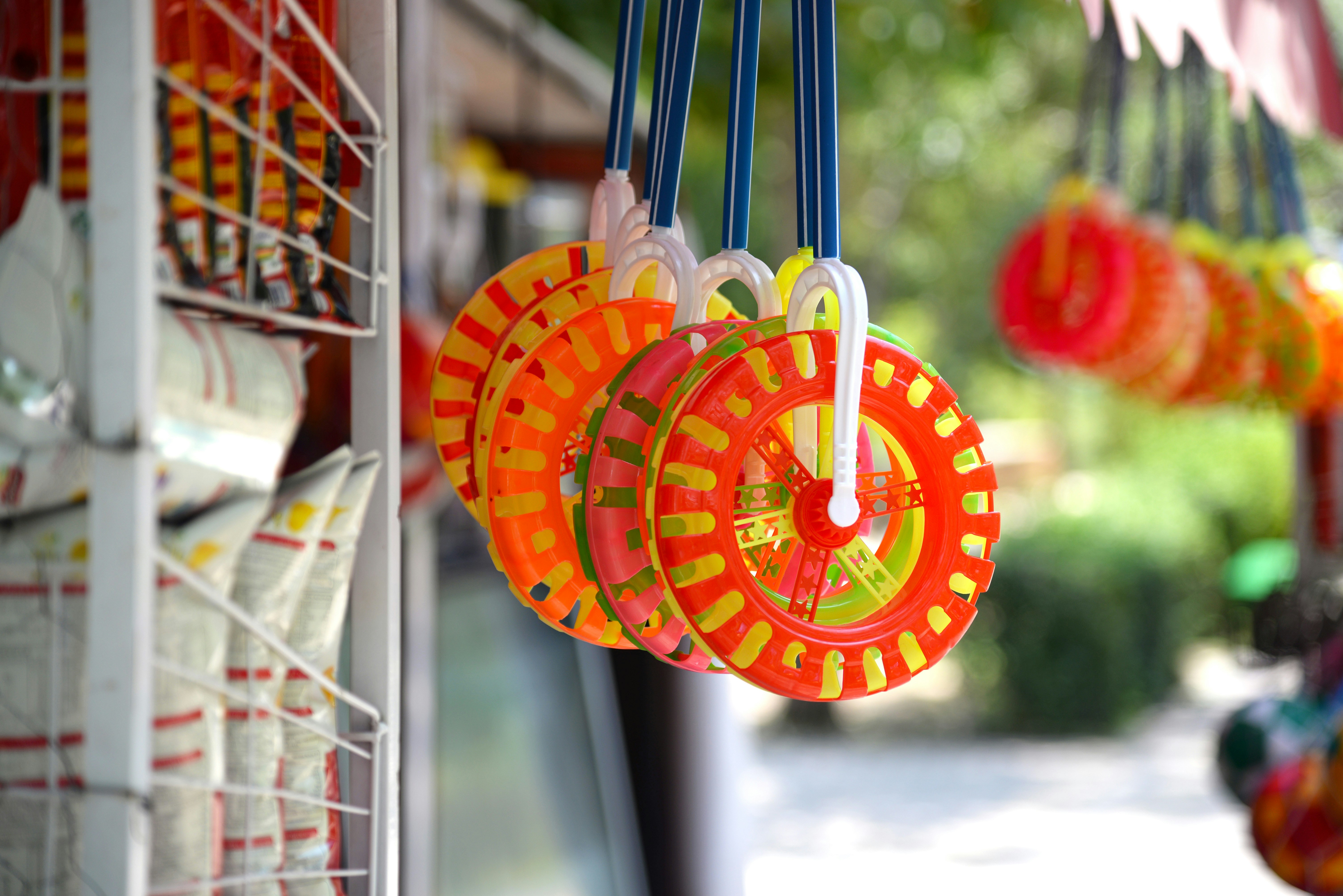 Several colorful, wheeled play items for children hanging in front of a booth in one of Tehran’s parks. | Colorful toys are hanging up for sale.