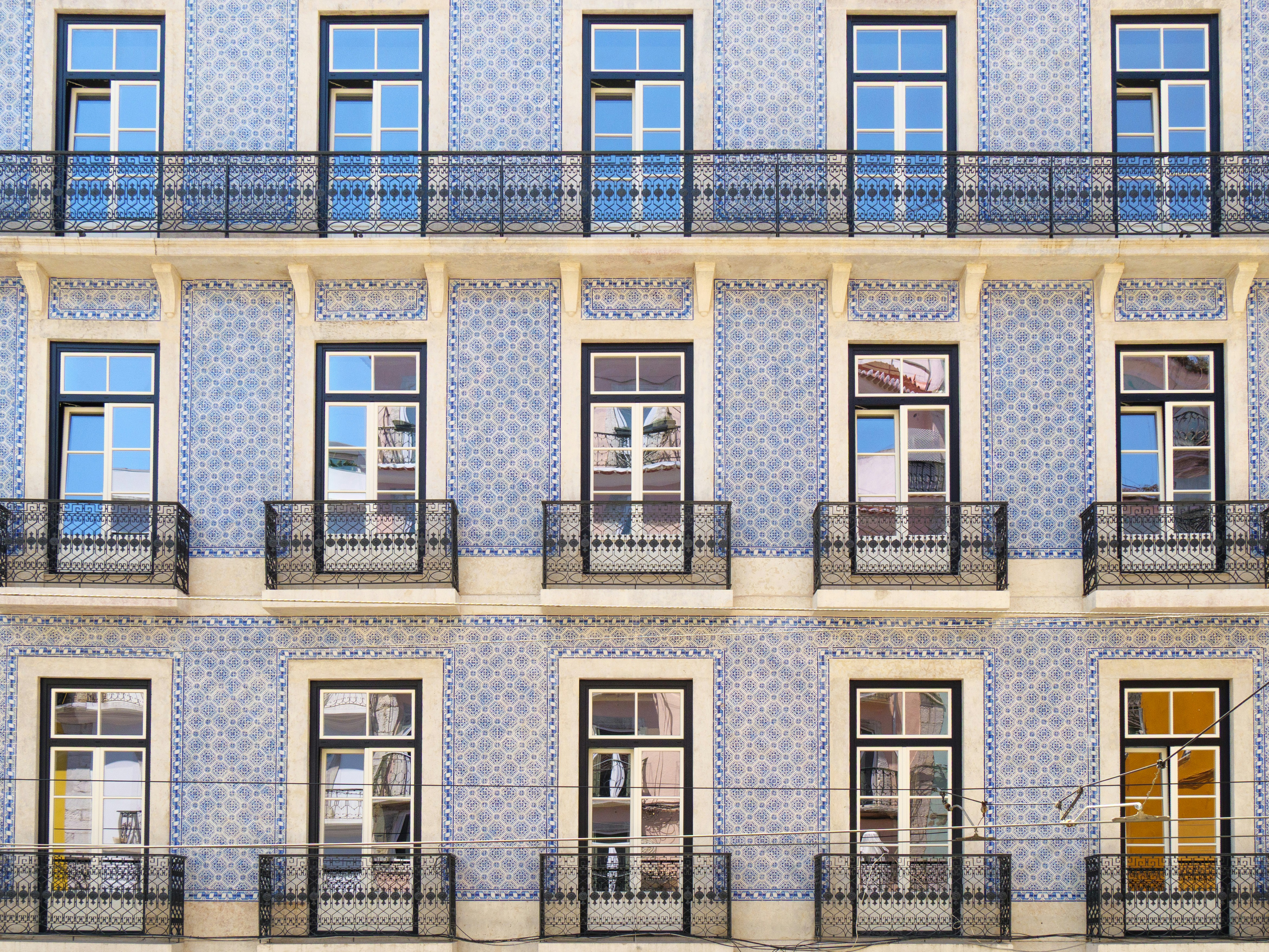 Intricate blue-tiled building facade adorned with multiple windows and wrought iron balconies, showcasing architectural elegance.