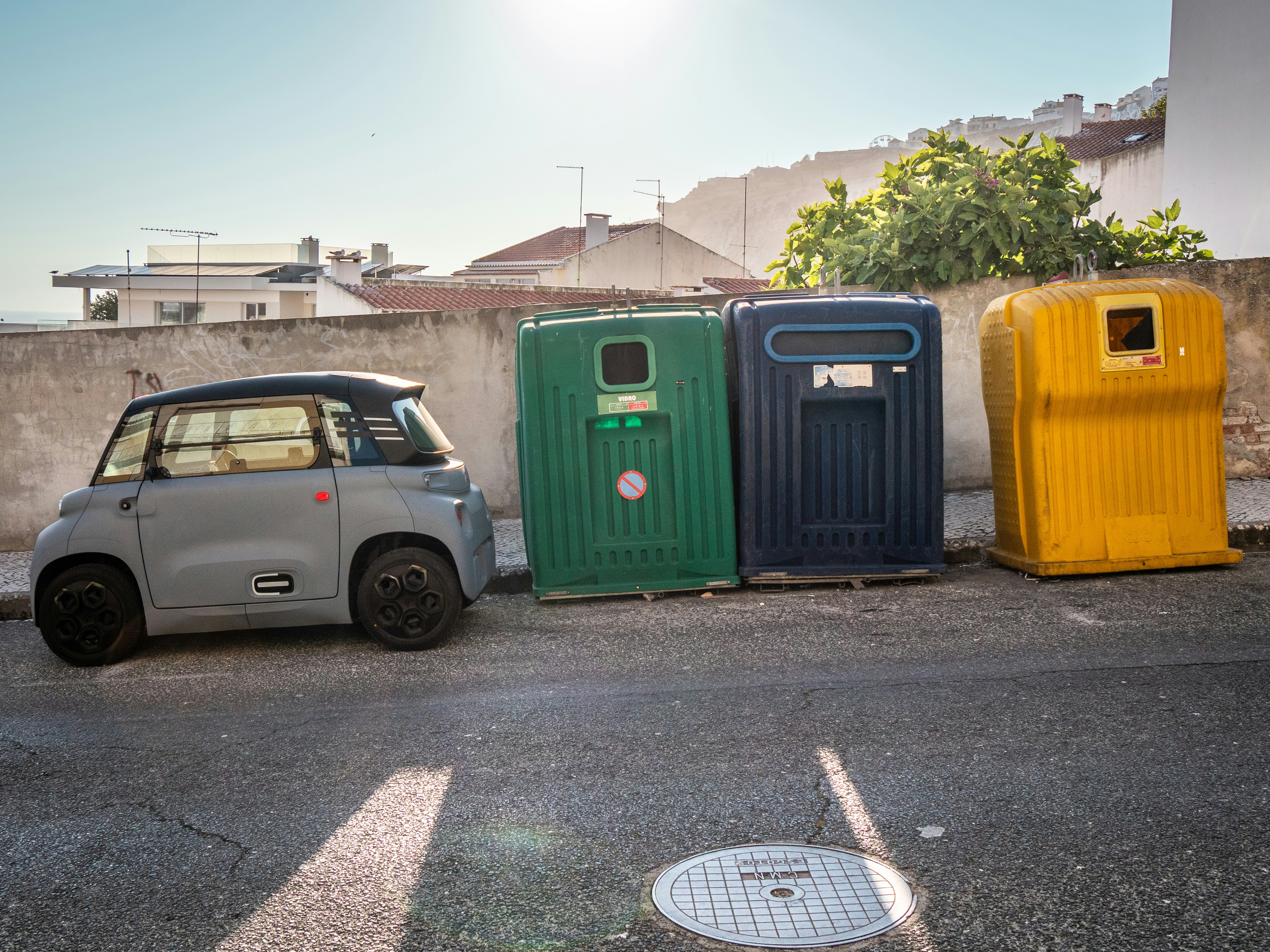 Urban Harmony: A Modern Vehicle Meets Colorful Recycling Bins