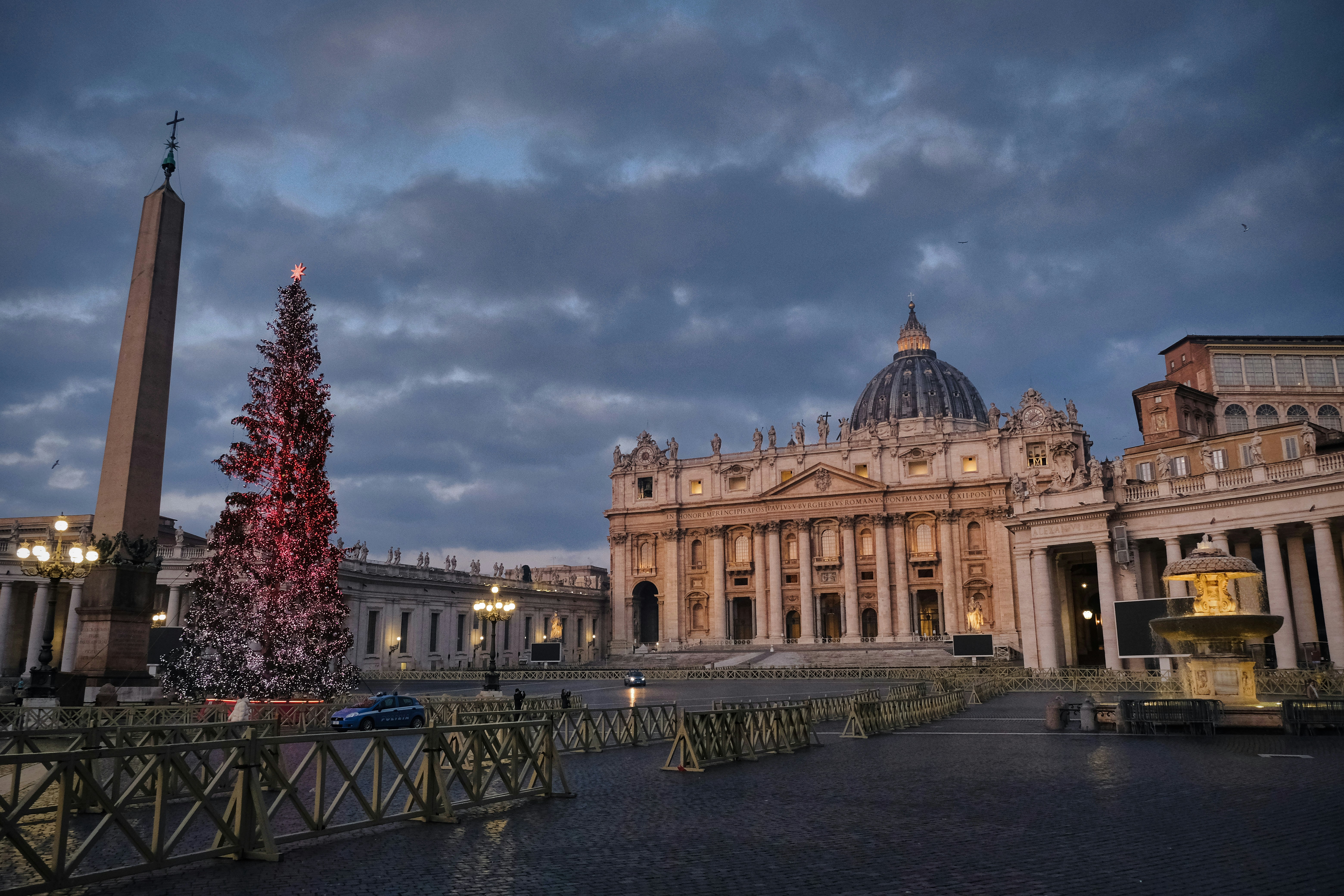 A quiet winter evening at St. Peter’s Square in Vatican City, with a glowing Christmas tree standing beside the majestic St. Peter’s Basilica. The festive lights and dramatic skies highlight the calm, sacred atmosphere of this iconic site during the holiday season. | Christmas tree in front of st. peter's basilica.