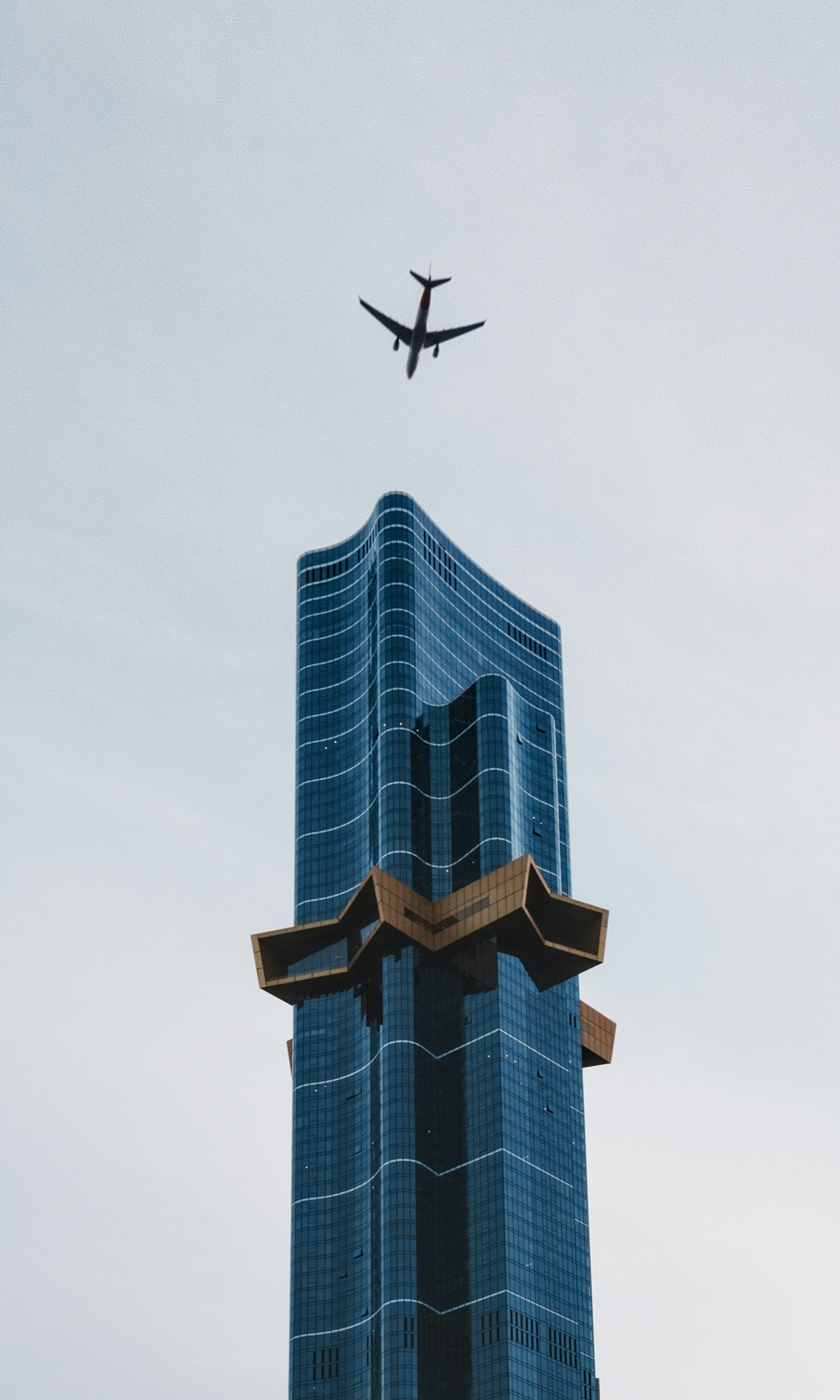 An airplane flies over a tall skyscraper.
