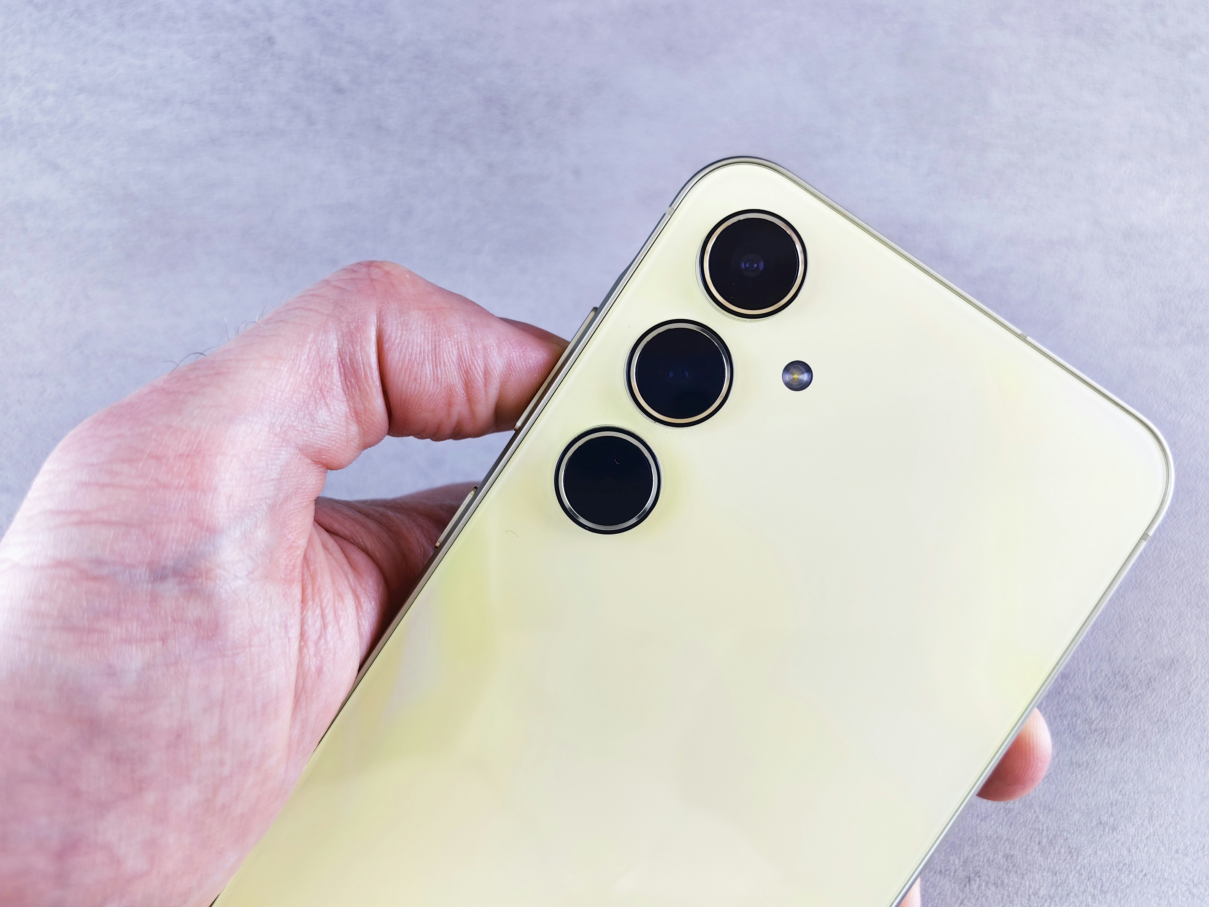 A hand holds a yellow smartphone with cameras.