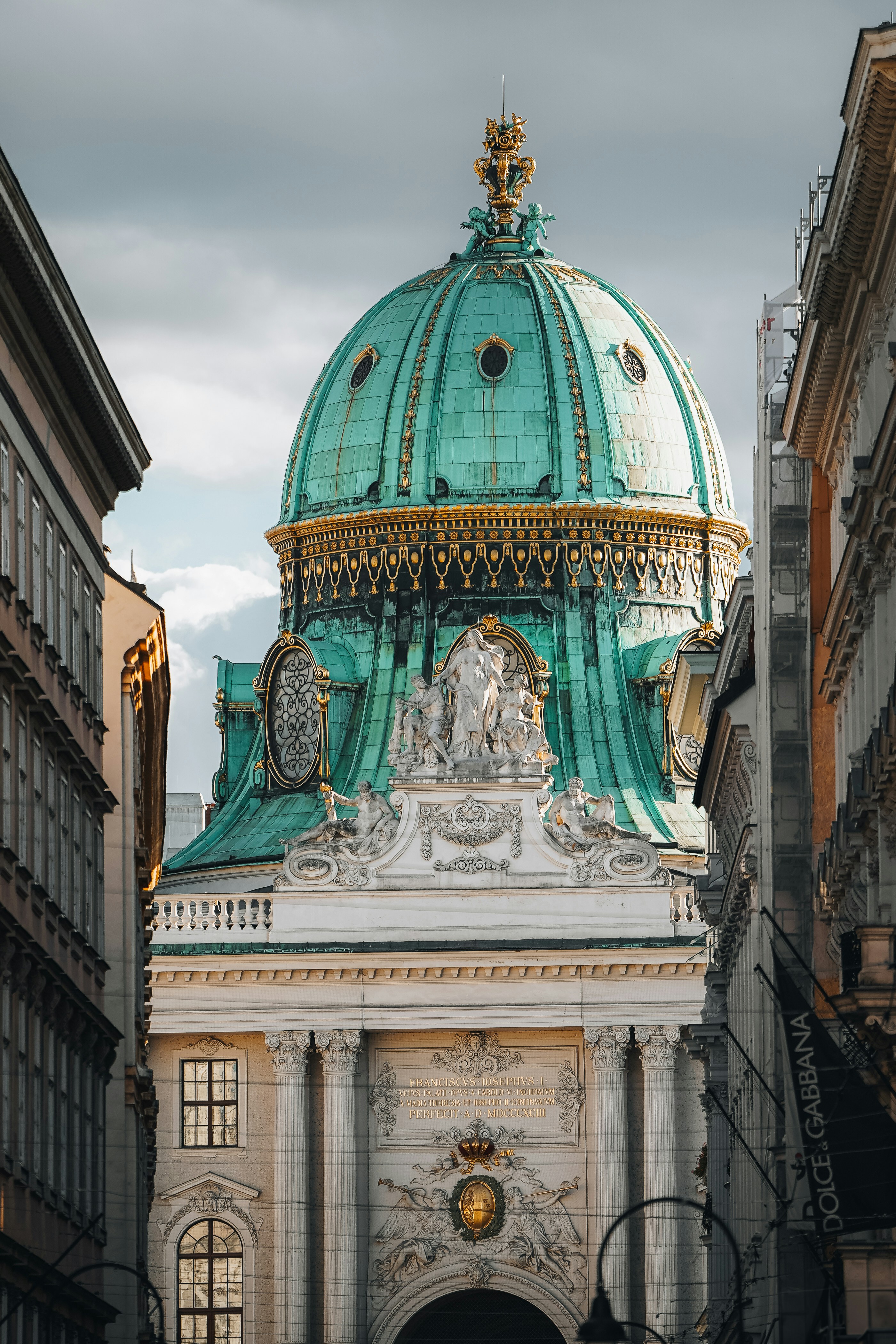 The green-copper dome rises between narrow facades, commanding attention like a crown nestled in the heart of Vienna’s old town. | A beautiful building with a green dome.