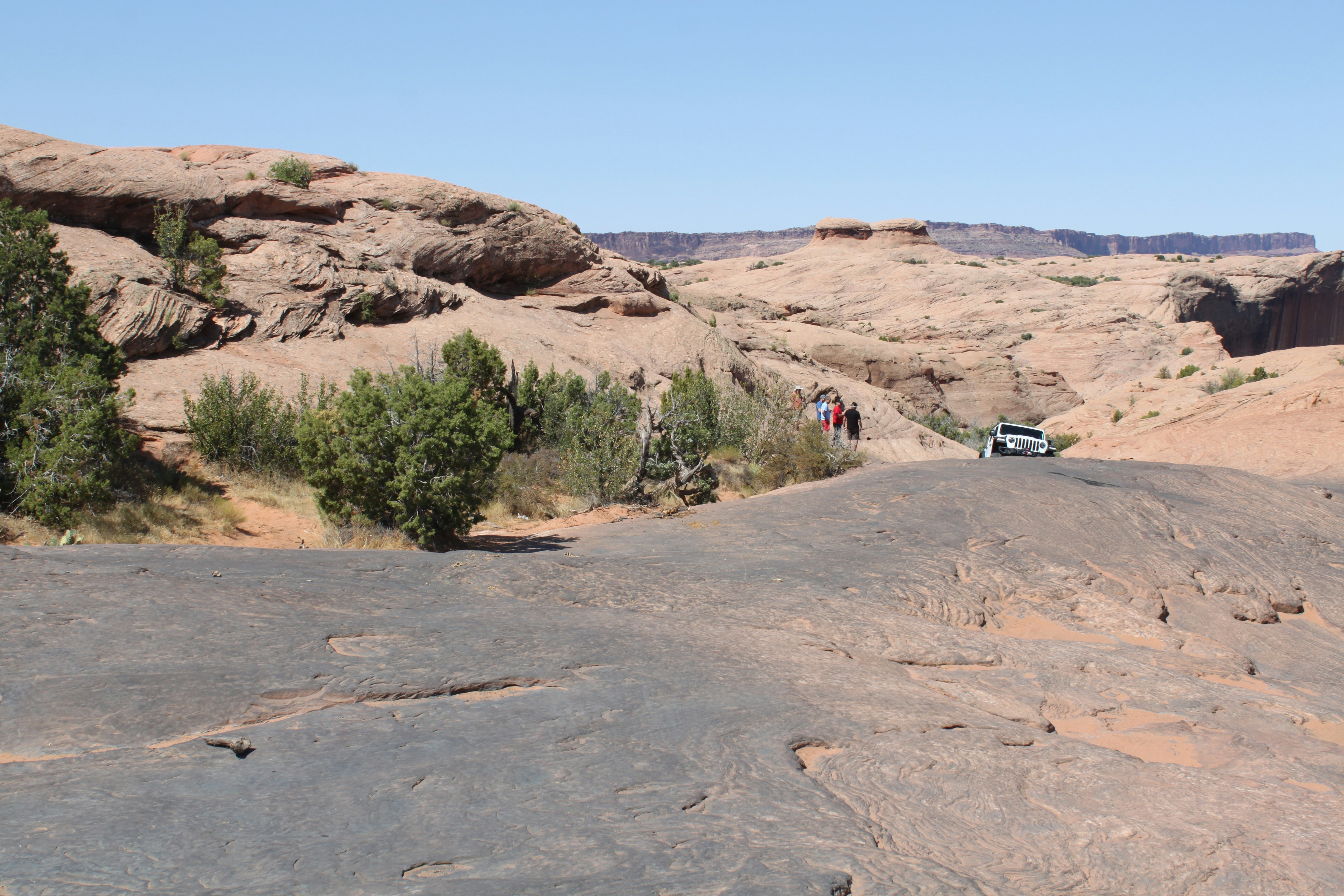 Desert Parkway: Cars and hikers on a sunlit cairn-lined canyon road