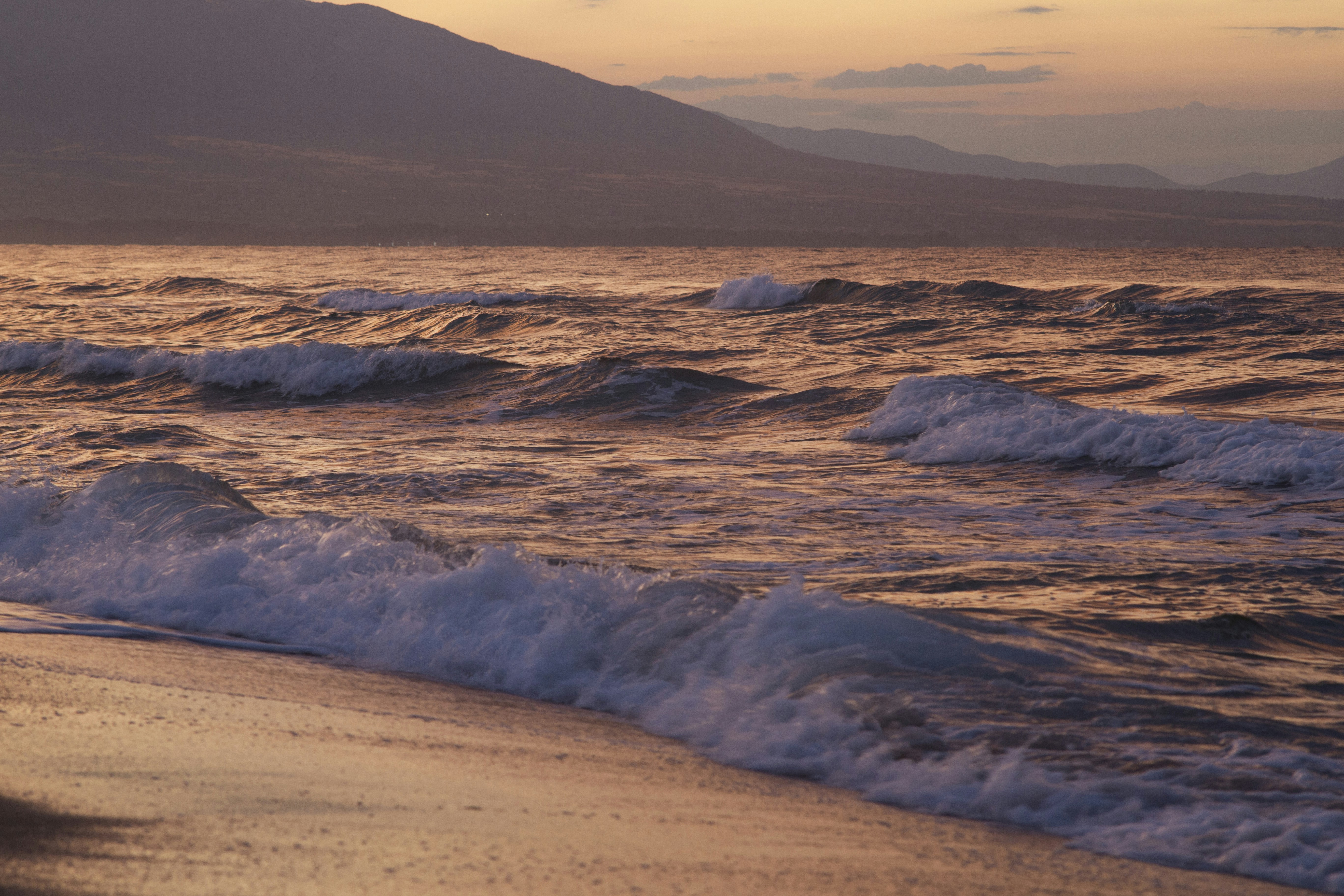 Waves crash on a beach at sunset.