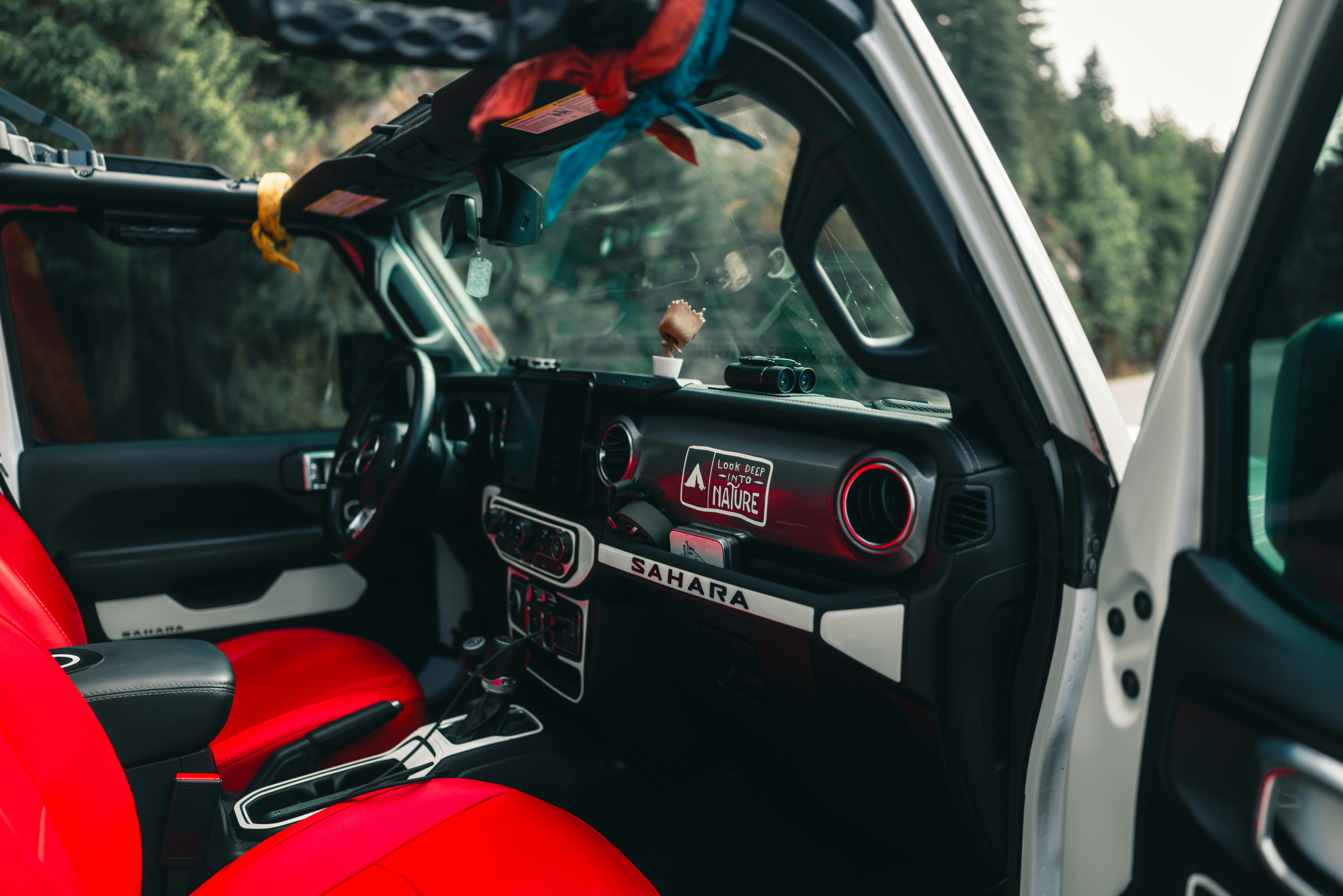 Interior view of a Jeep Wrangler Sahara featuring striking red seats and a dashboard adorned with adventure-themed decor.