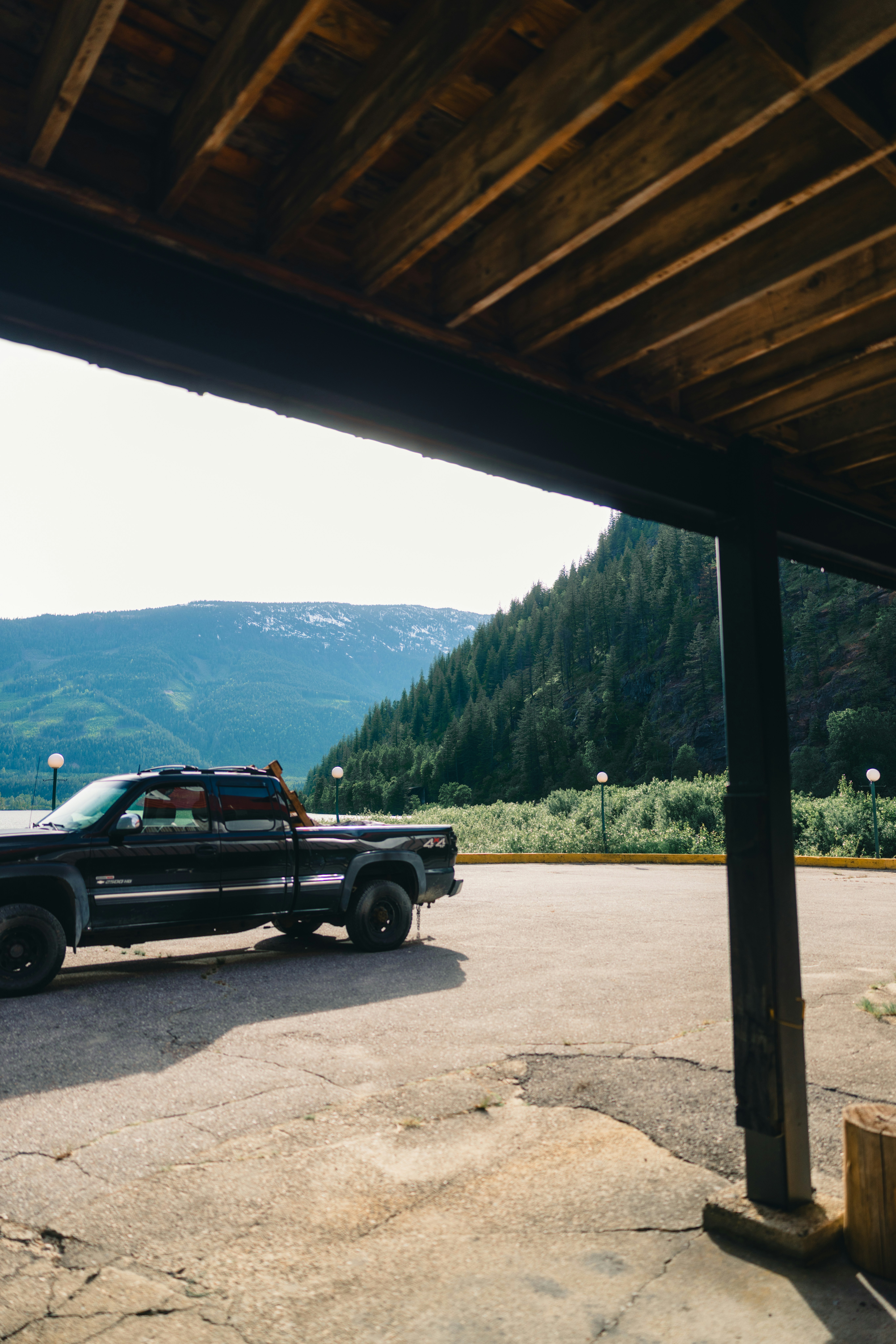Black pickup truck parked near a scenic mountain backdrop, framed by wooden structure. Lush greenery and distant mountains create a serene atmosphere.