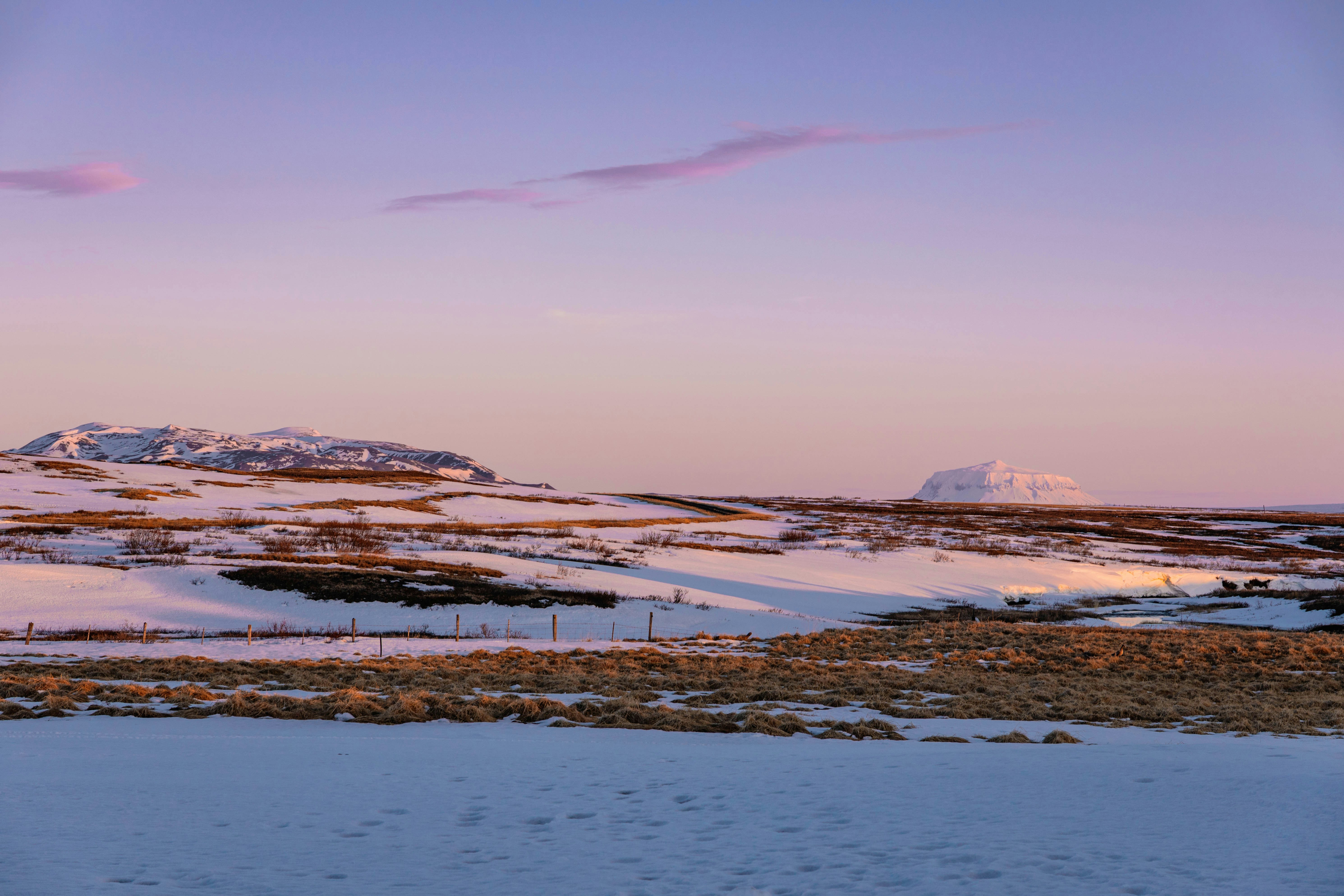Snow-covered landscape with mountains under a pink sky.
