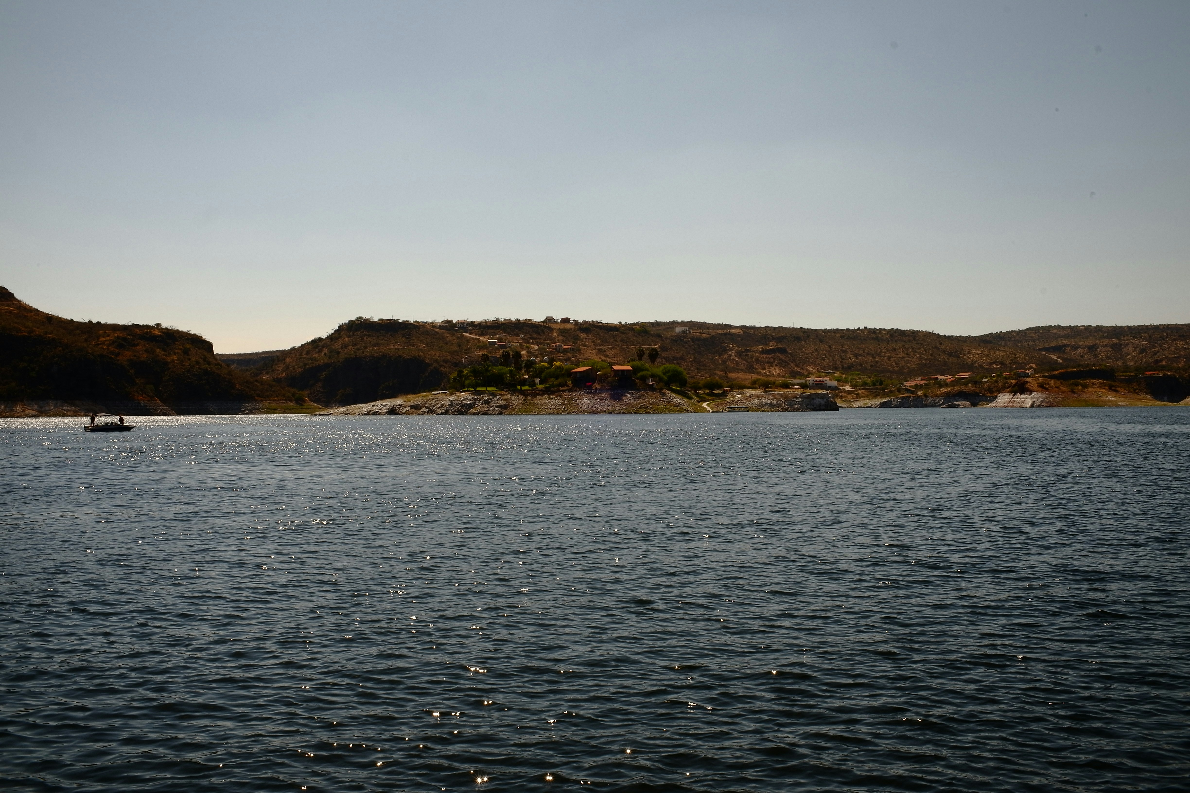 The calm lake reflects the hazy, sunny landscape.