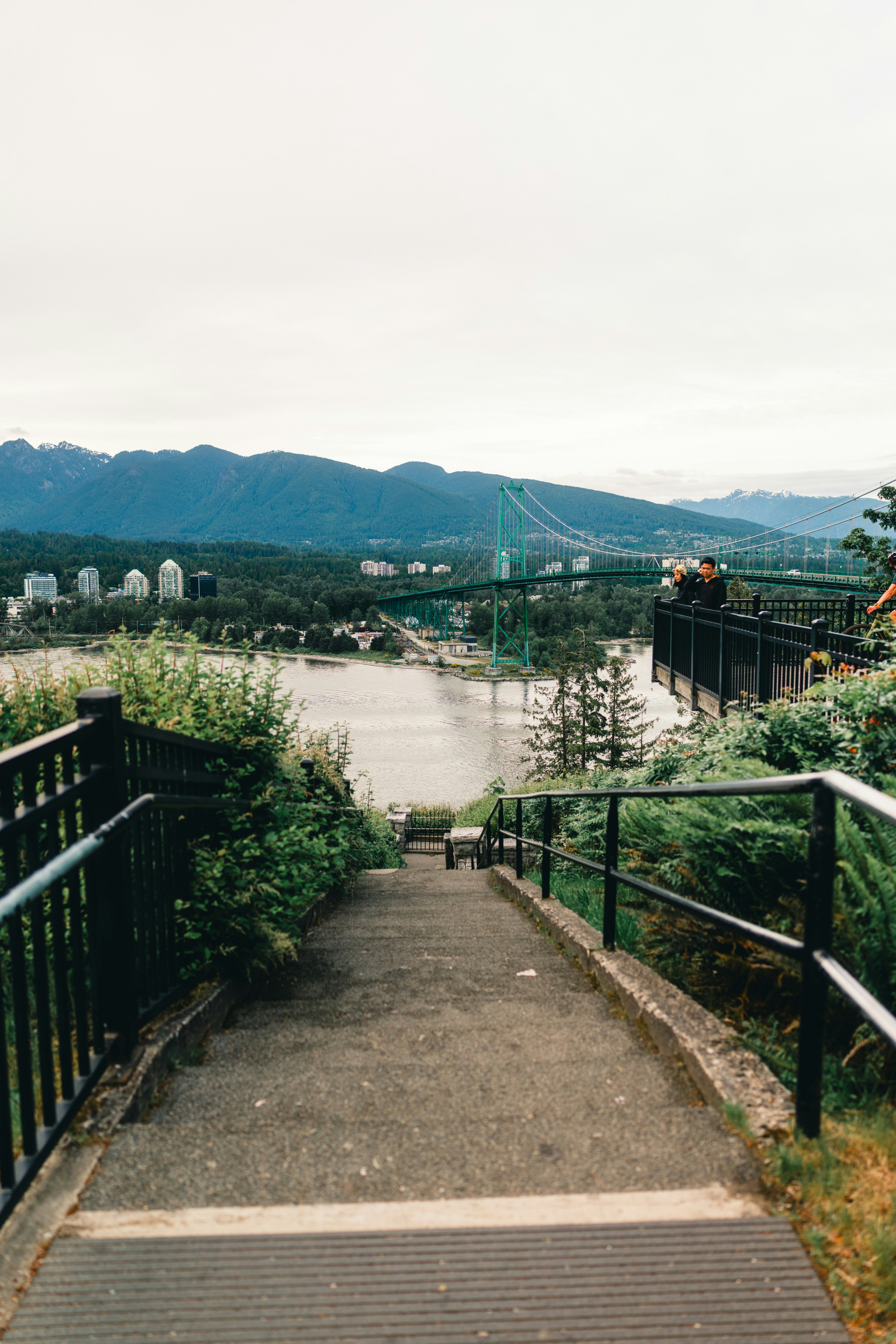 Footpath to the Riverside Vista Under a Green Suspension Bridge