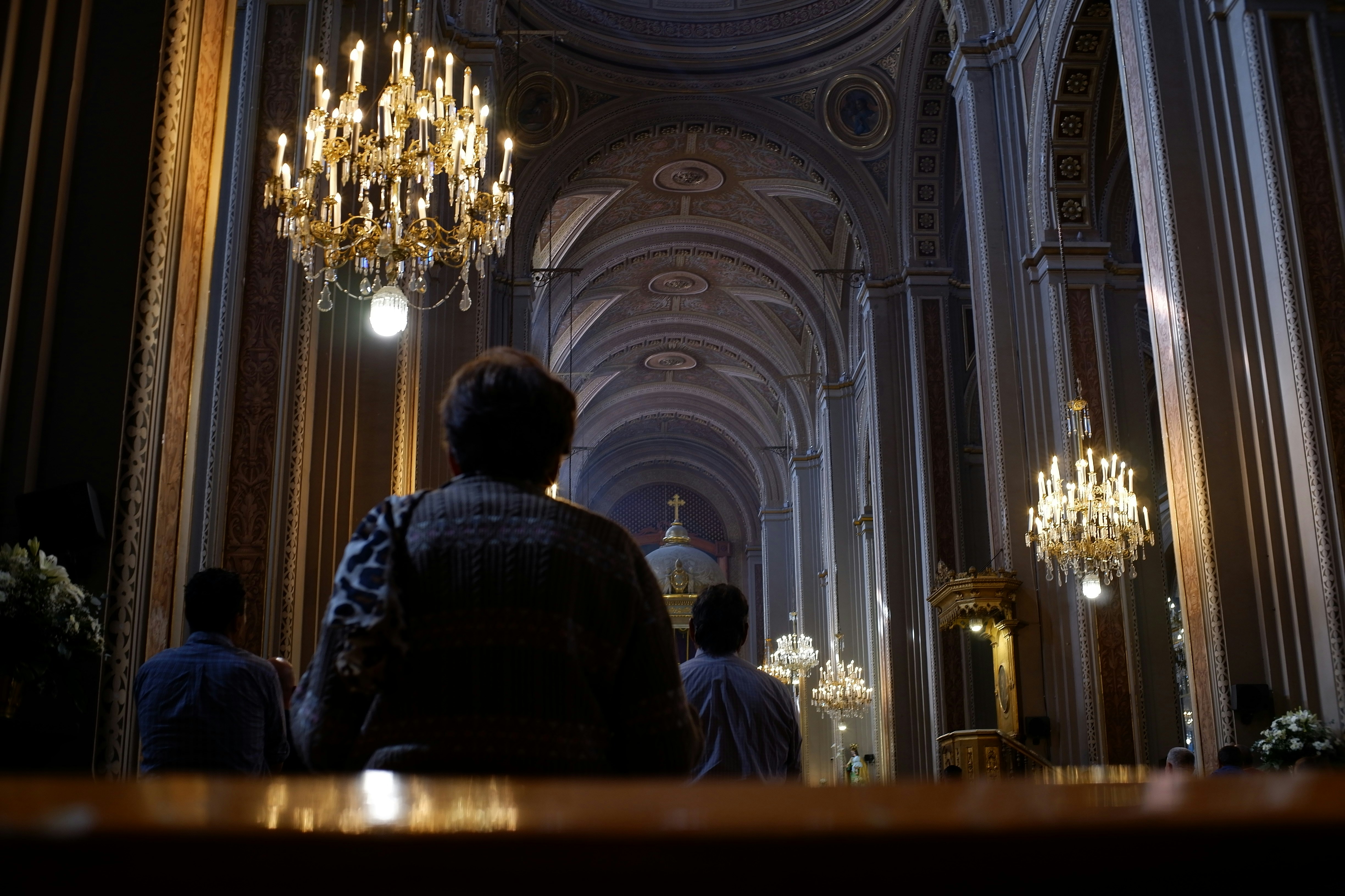 A serene interior of a grand church, featuring elegant chandeliers and towering arches, with a figure in silhouette observing the space.