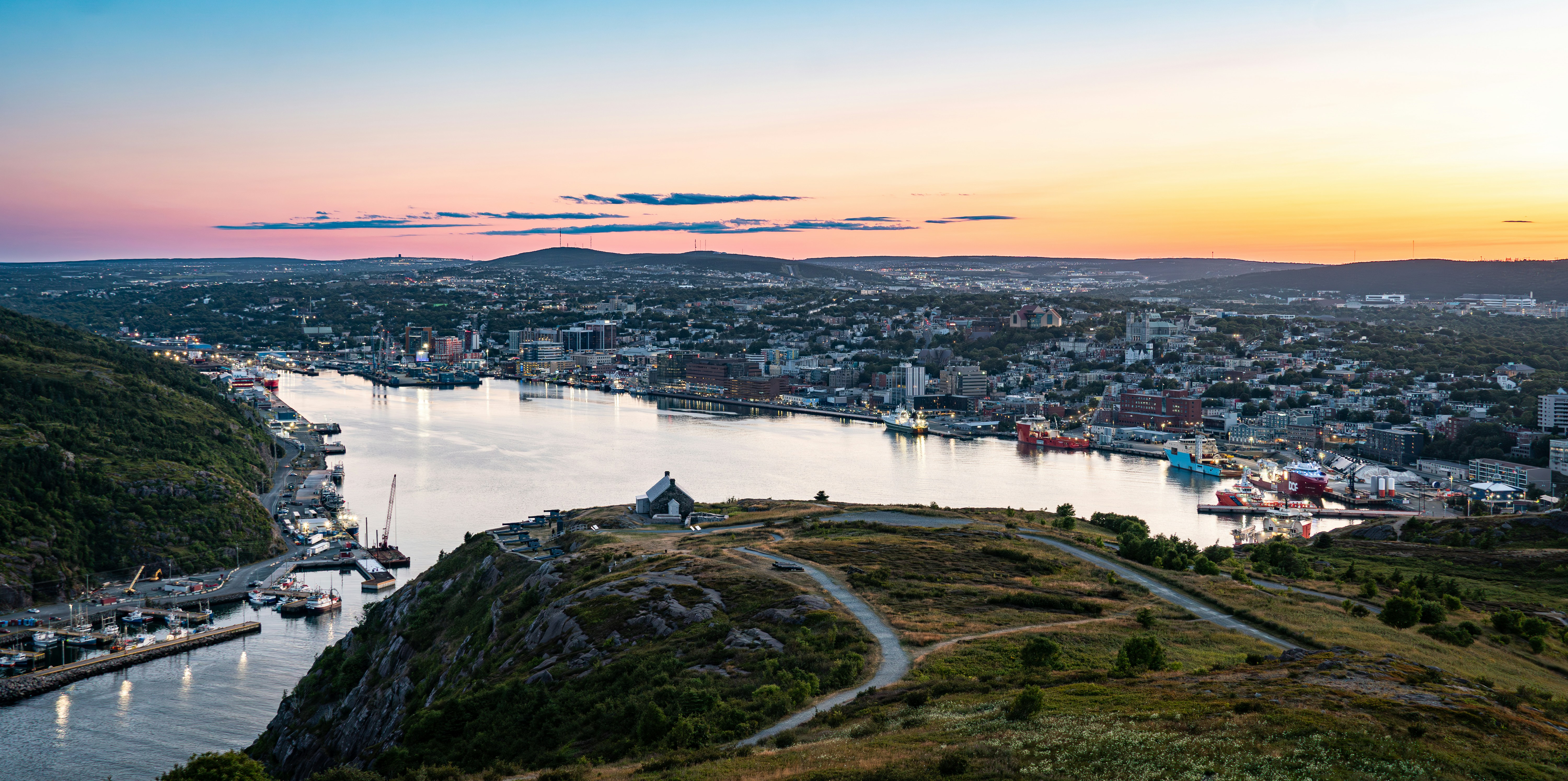 Panoramic view of a bustling harbor at twilight, showcasing the city’s lights reflecting on the water and the surrounding hills. 