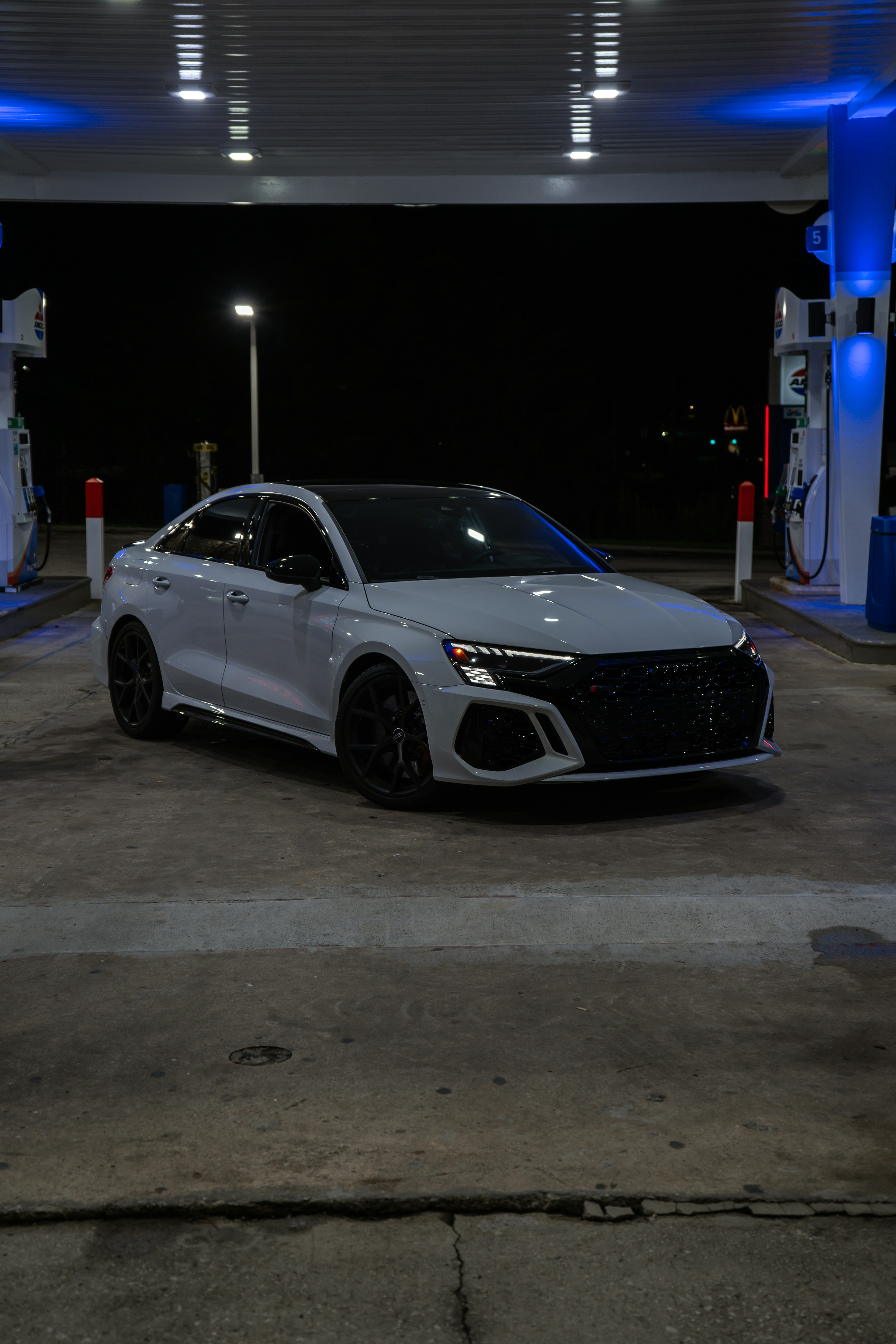 Sleek white sedan parked at a gas station under dramatic lighting, showcasing its stylish design against a nighttime backdrop.