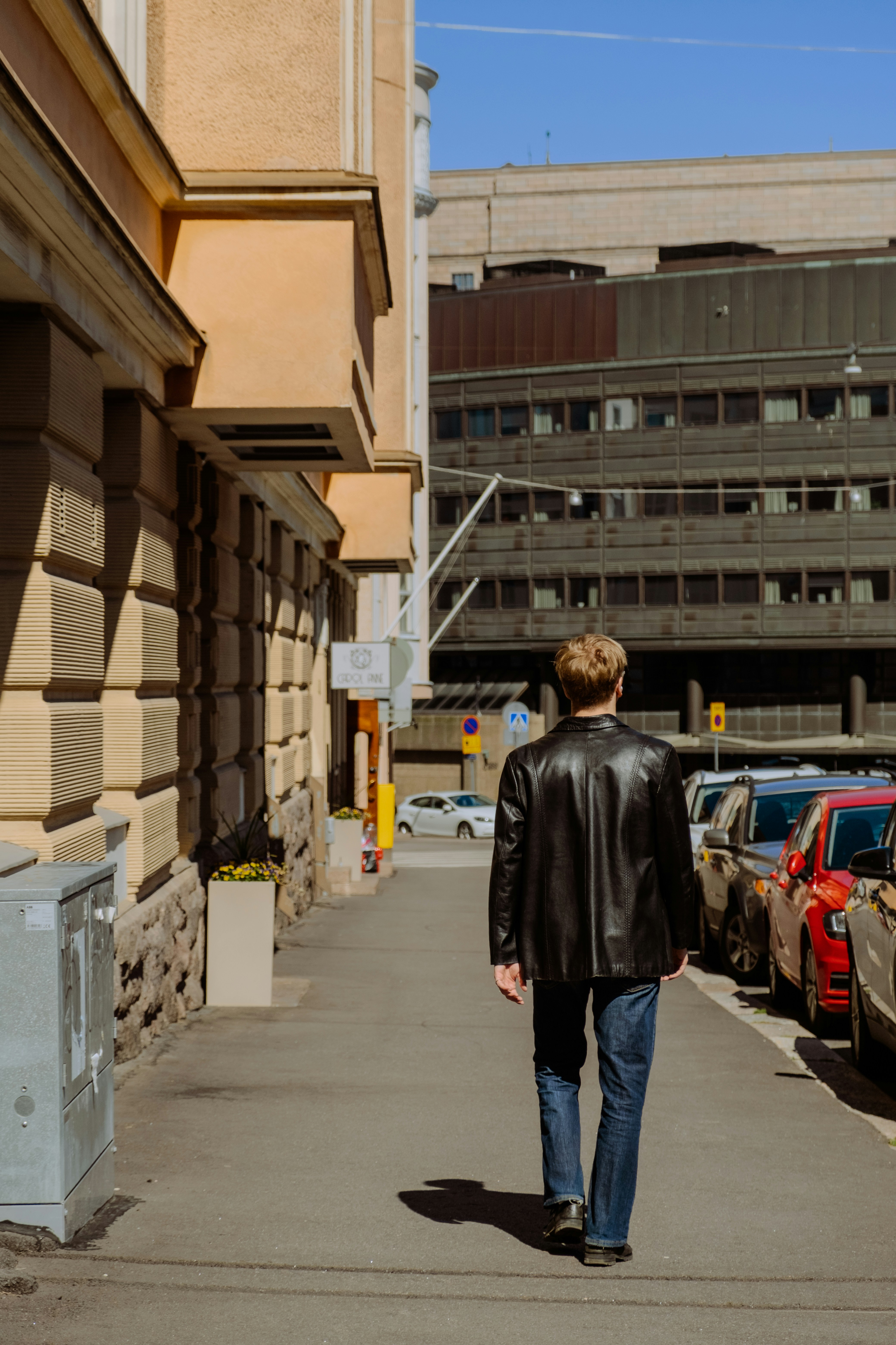 Traveler in a Leather Jacket Walks Through a Canyon of Urban Facades