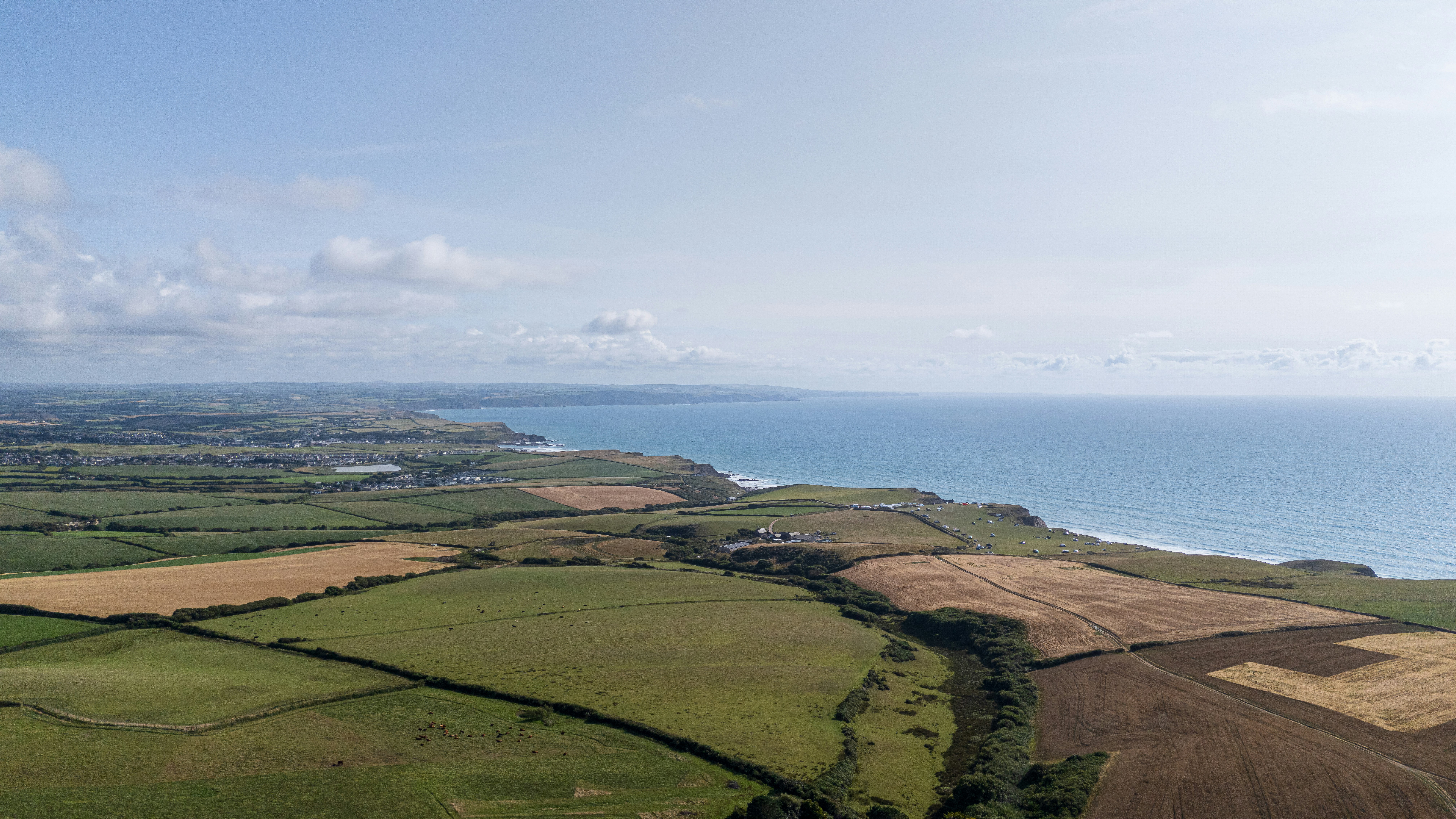 drone shot bude cornwall | Green fields meet the sea under a bright sky.