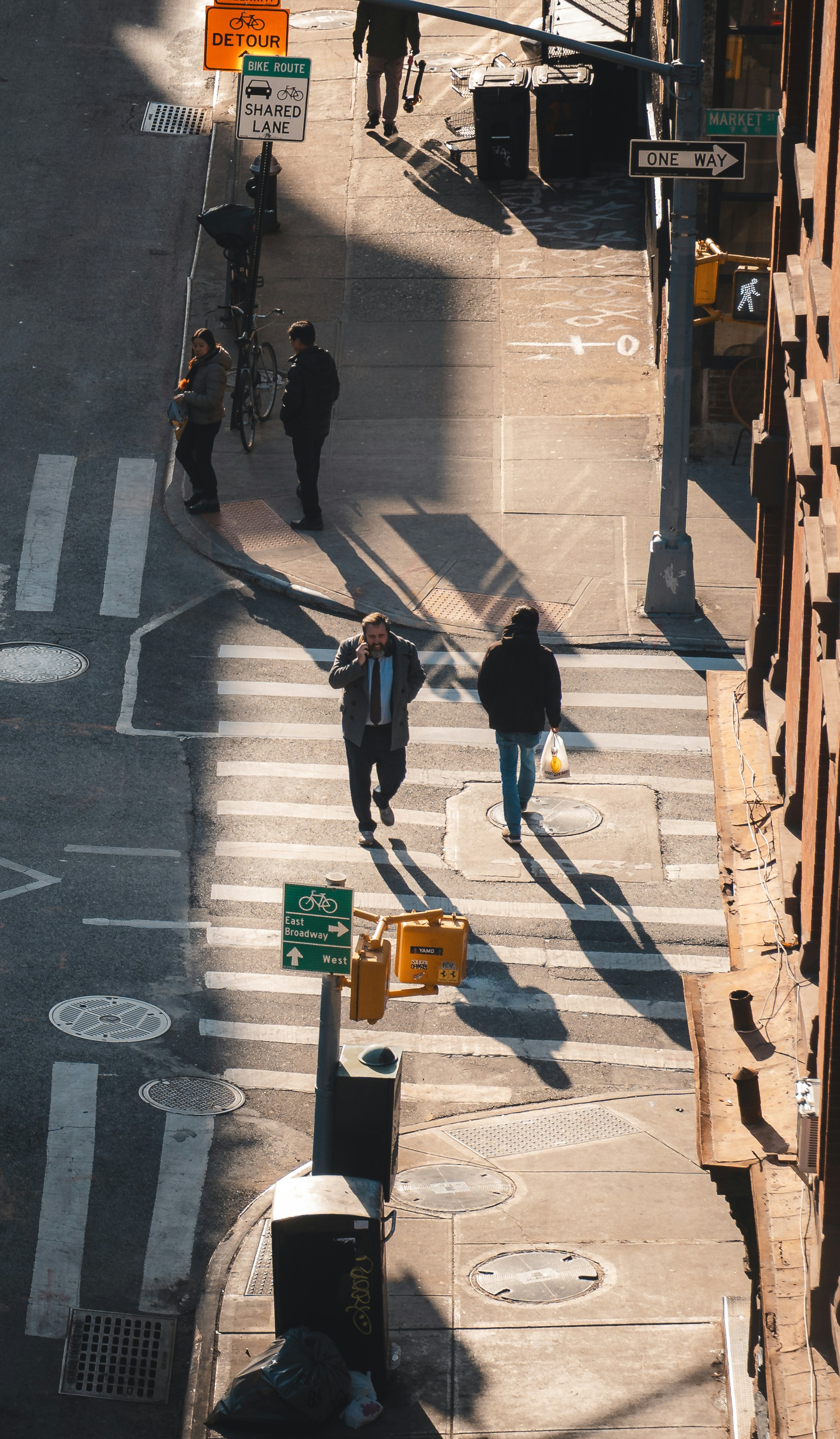 People walk across a street's crosswalk on a sunny day.