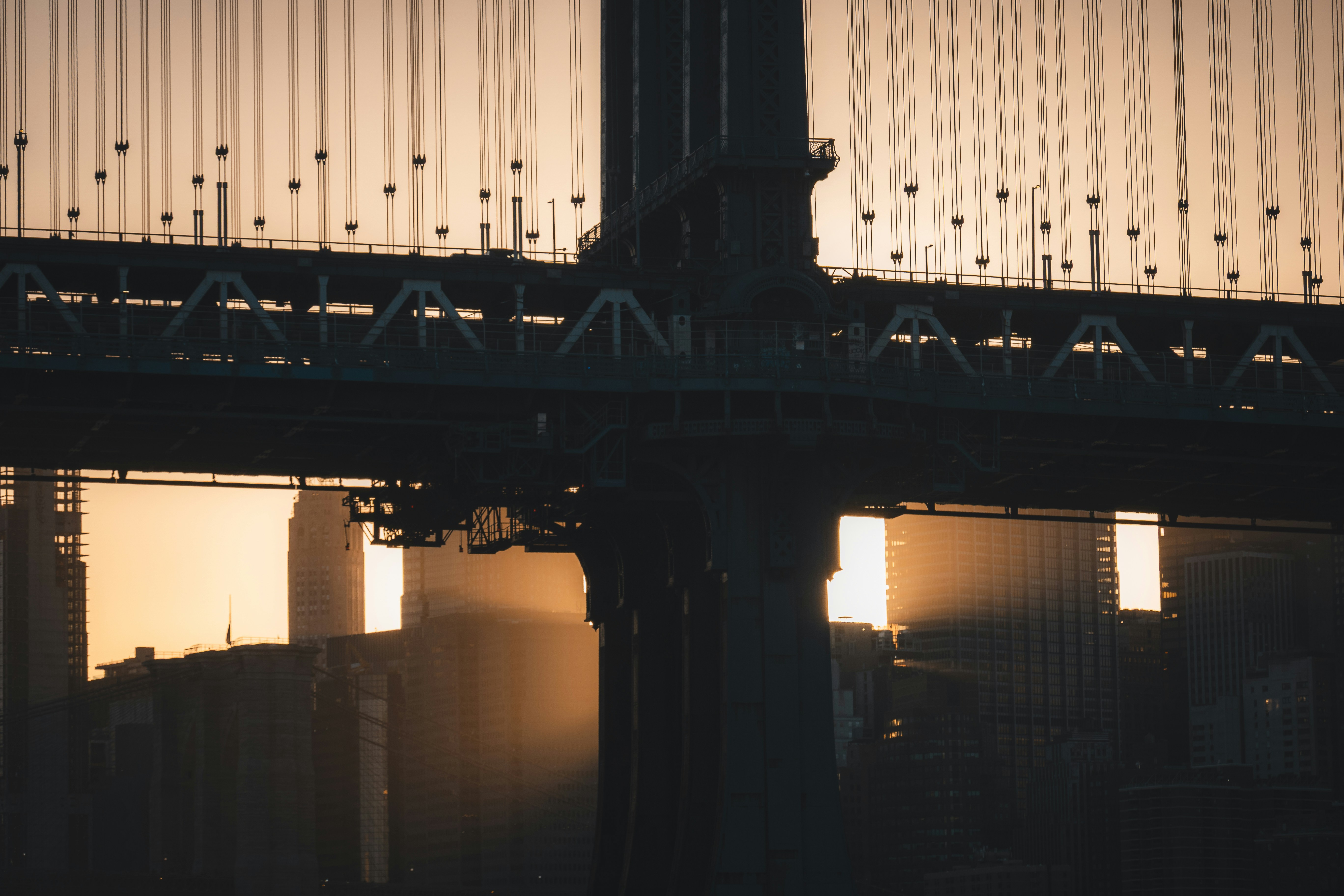 Silhouette of a bridge against a sunset, with city buildings partially illuminated in the background.