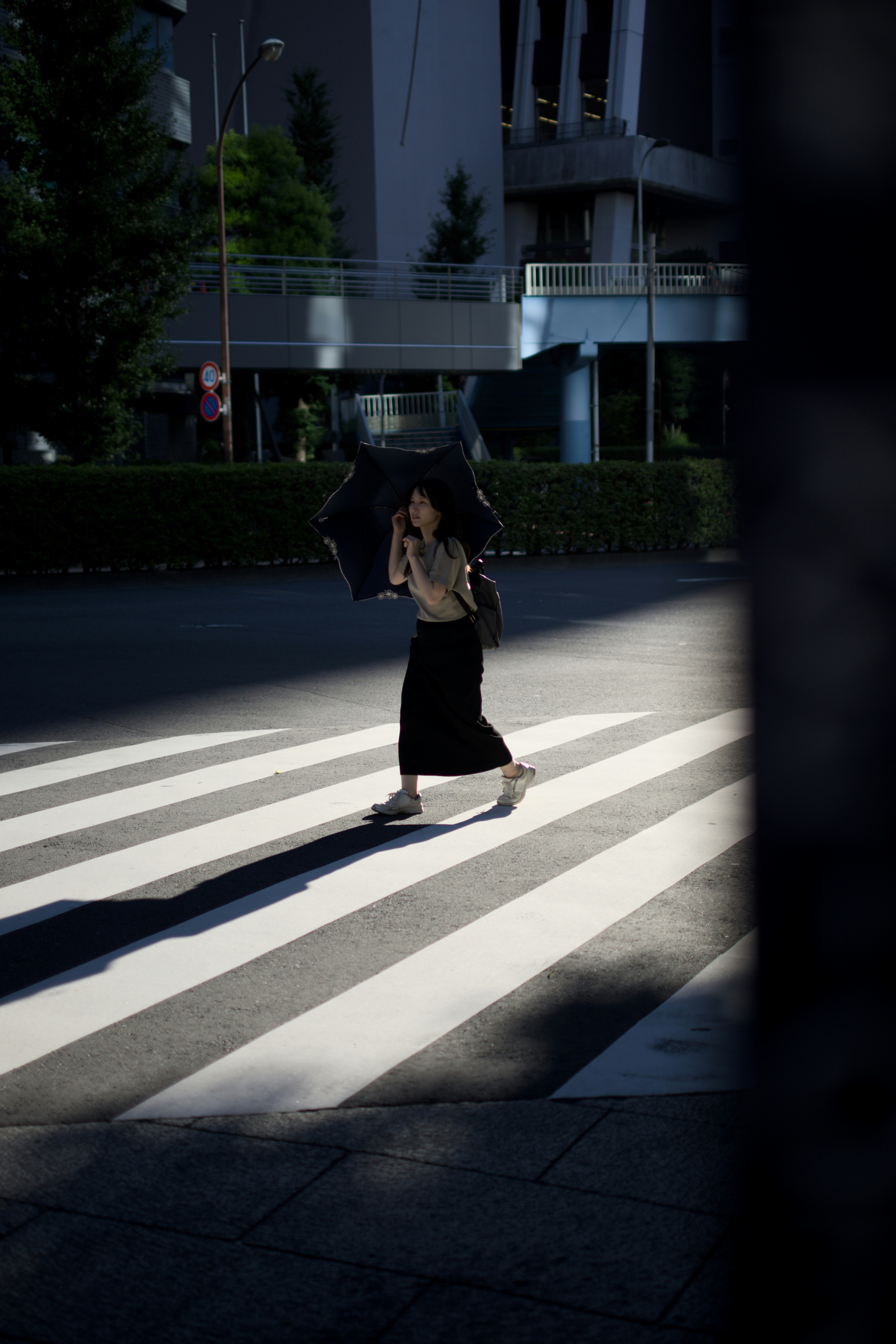 A woman crosses a street with an umbrella.