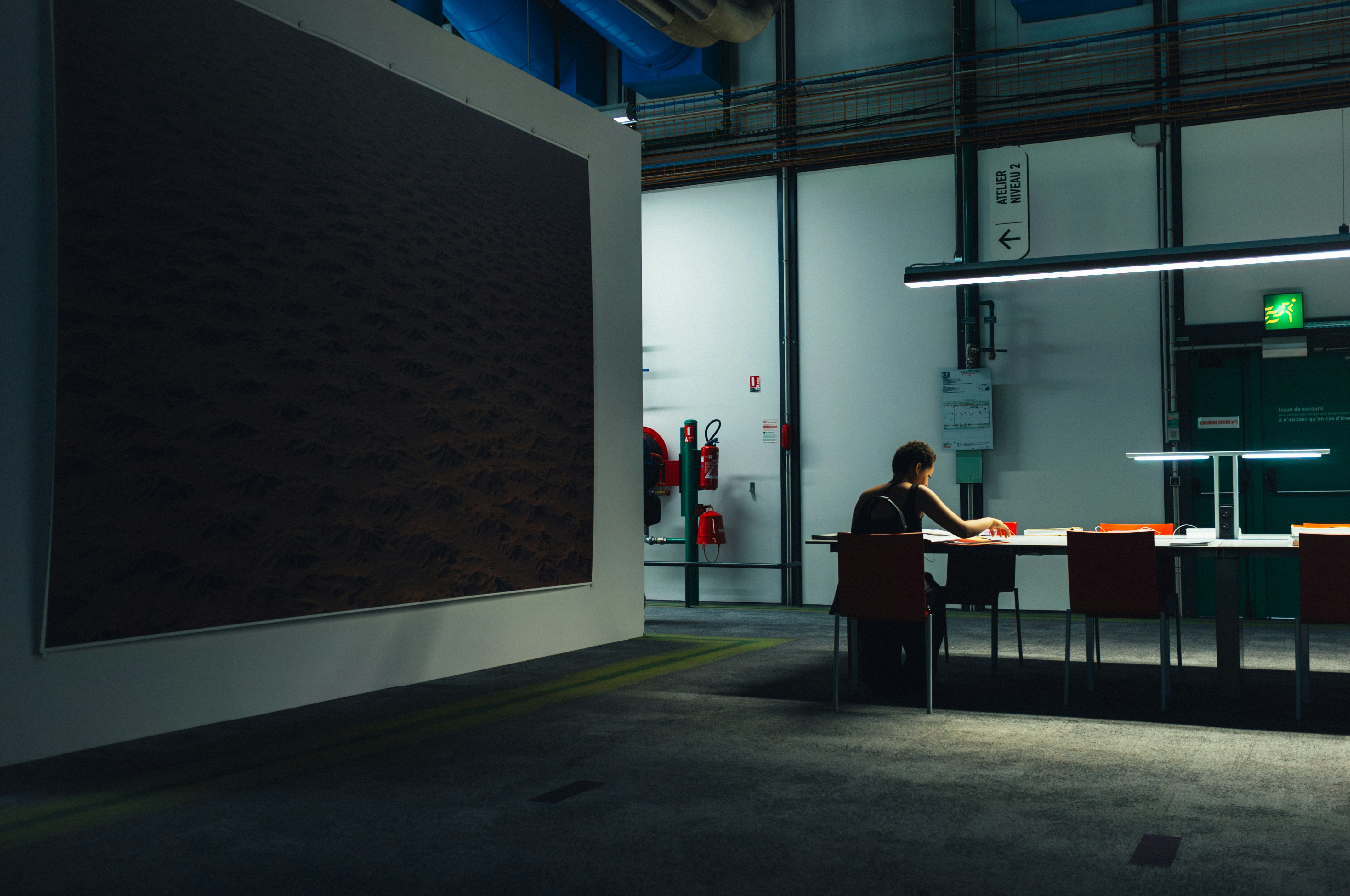 A person reads at a table in a dimly lit room.