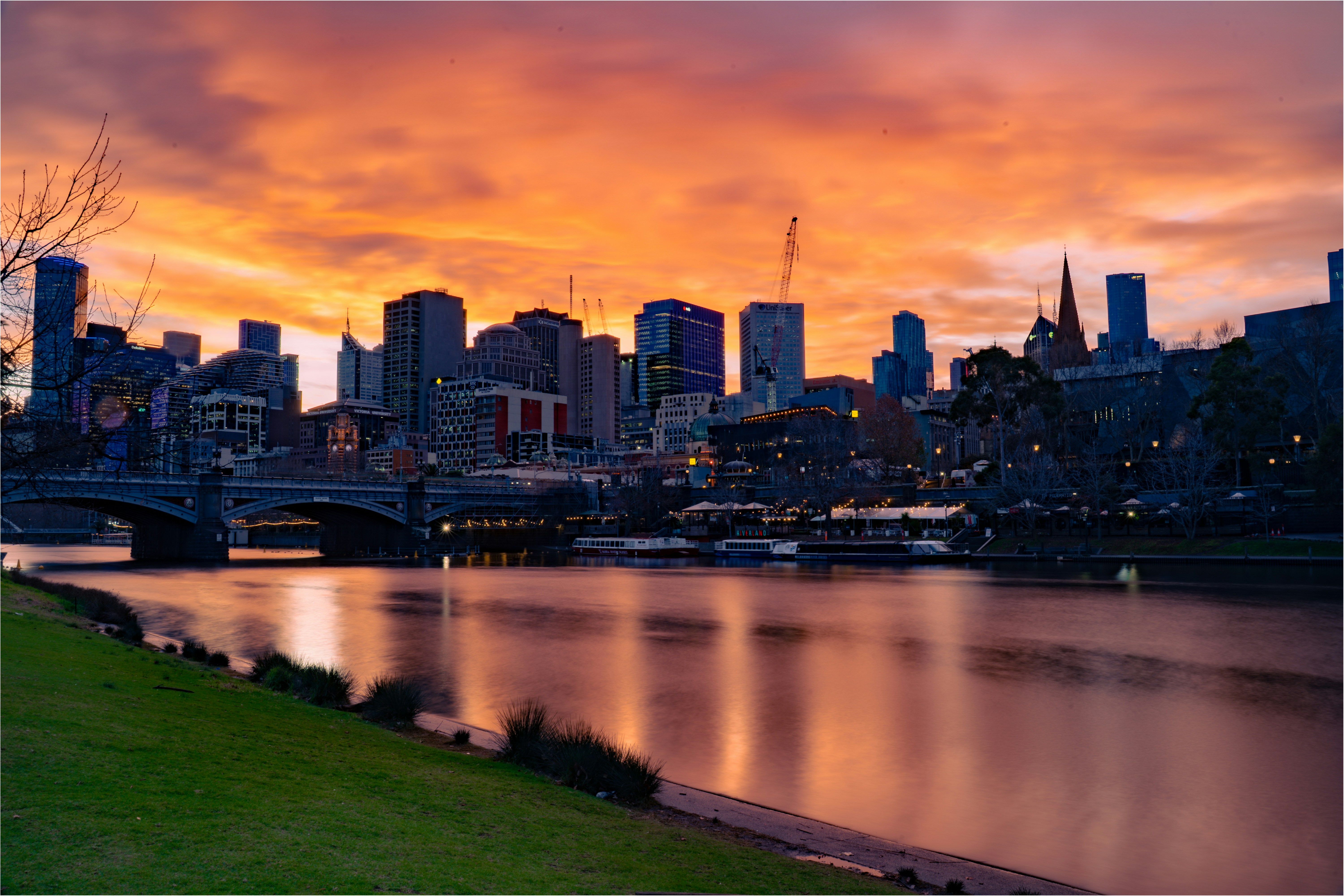 Vibrant sunset reflecting on the Yarra River with the Melbourne skyline in the background, showcasing a blend of modern architecture and natural beauty.