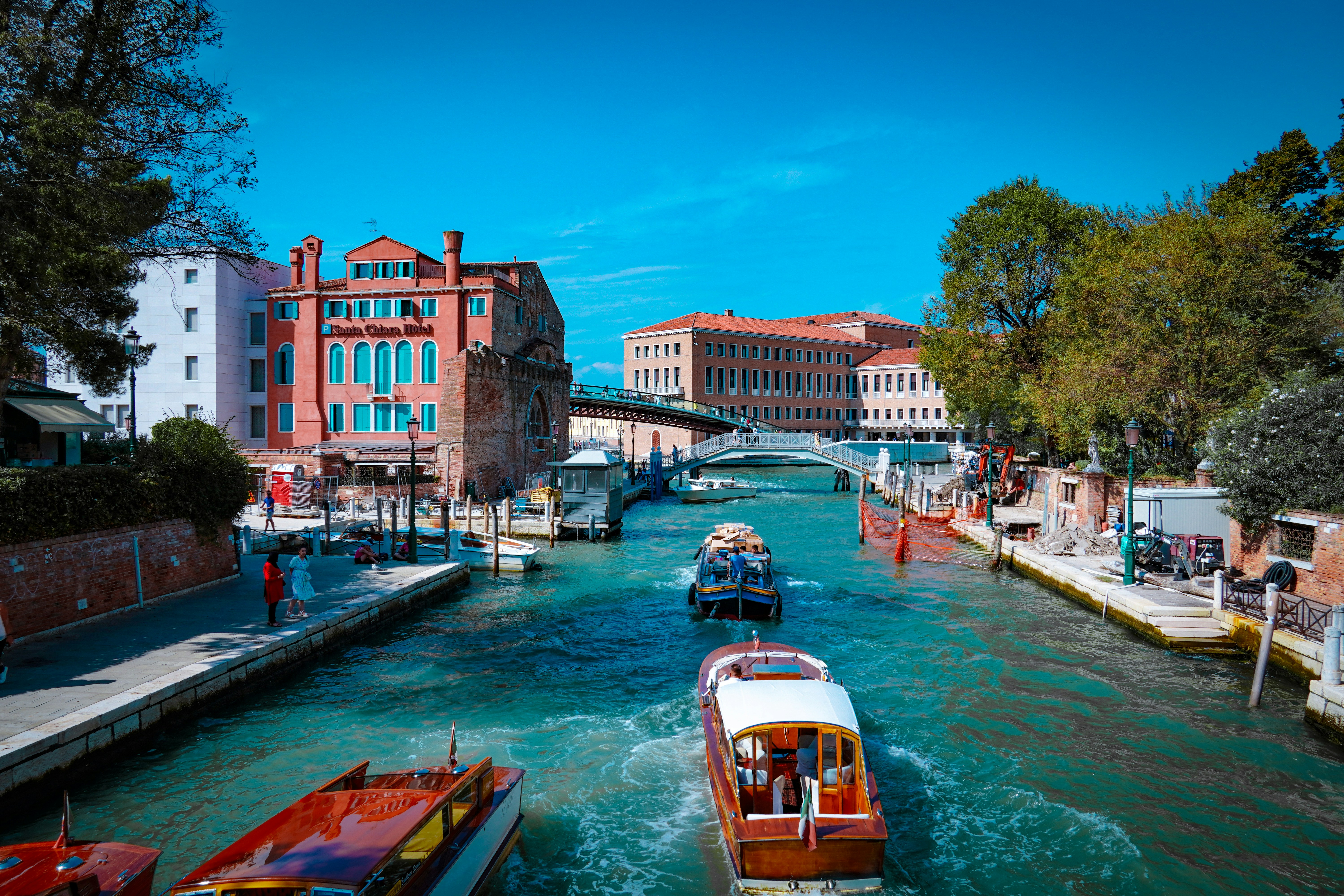 Boats navigate through the vibrant canals of Venice, framed by historic buildings and lush greenery. The scene captures the essence of everyday life in this iconic city.