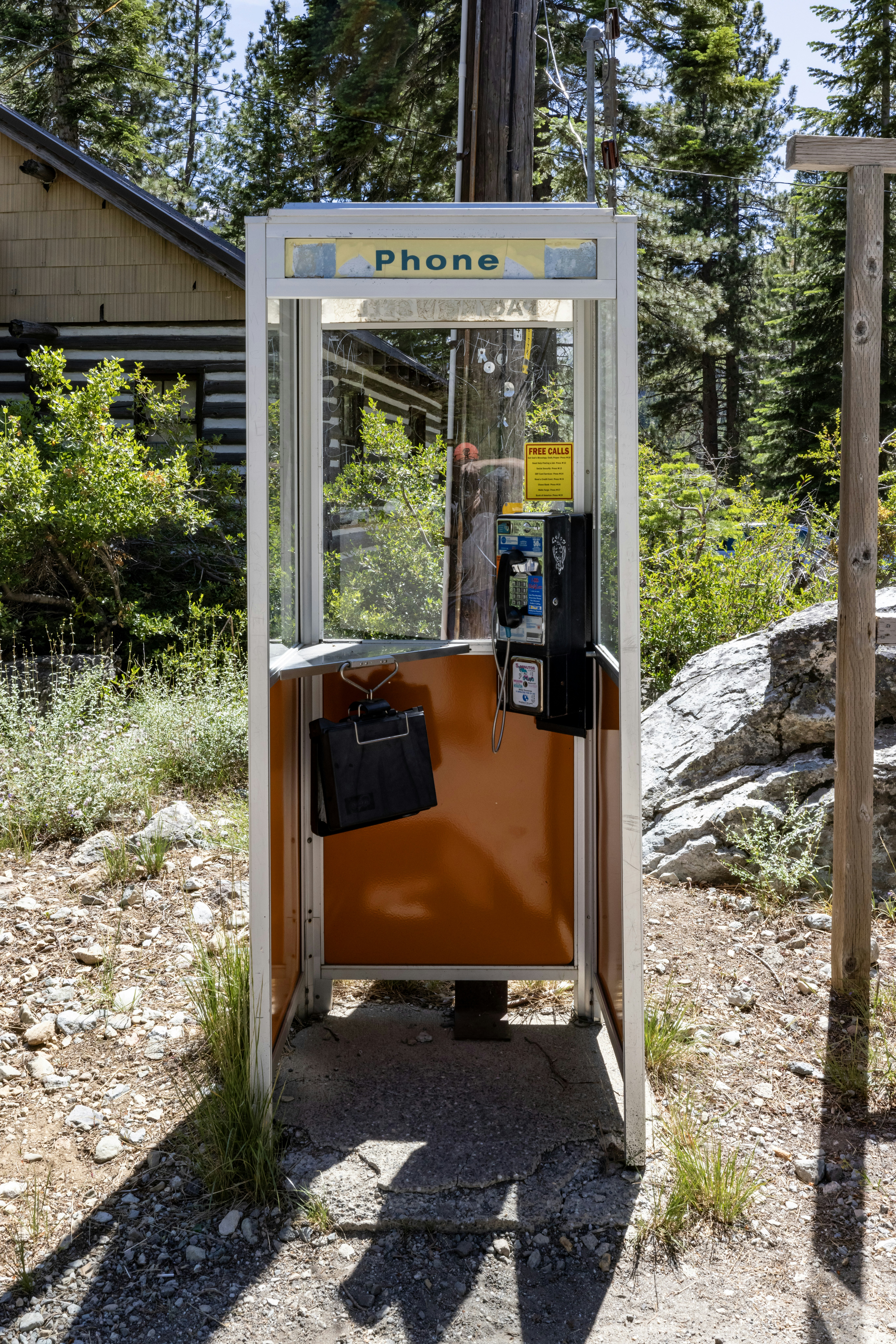 Phone book still intact. | An old telephone booth stands in nature.