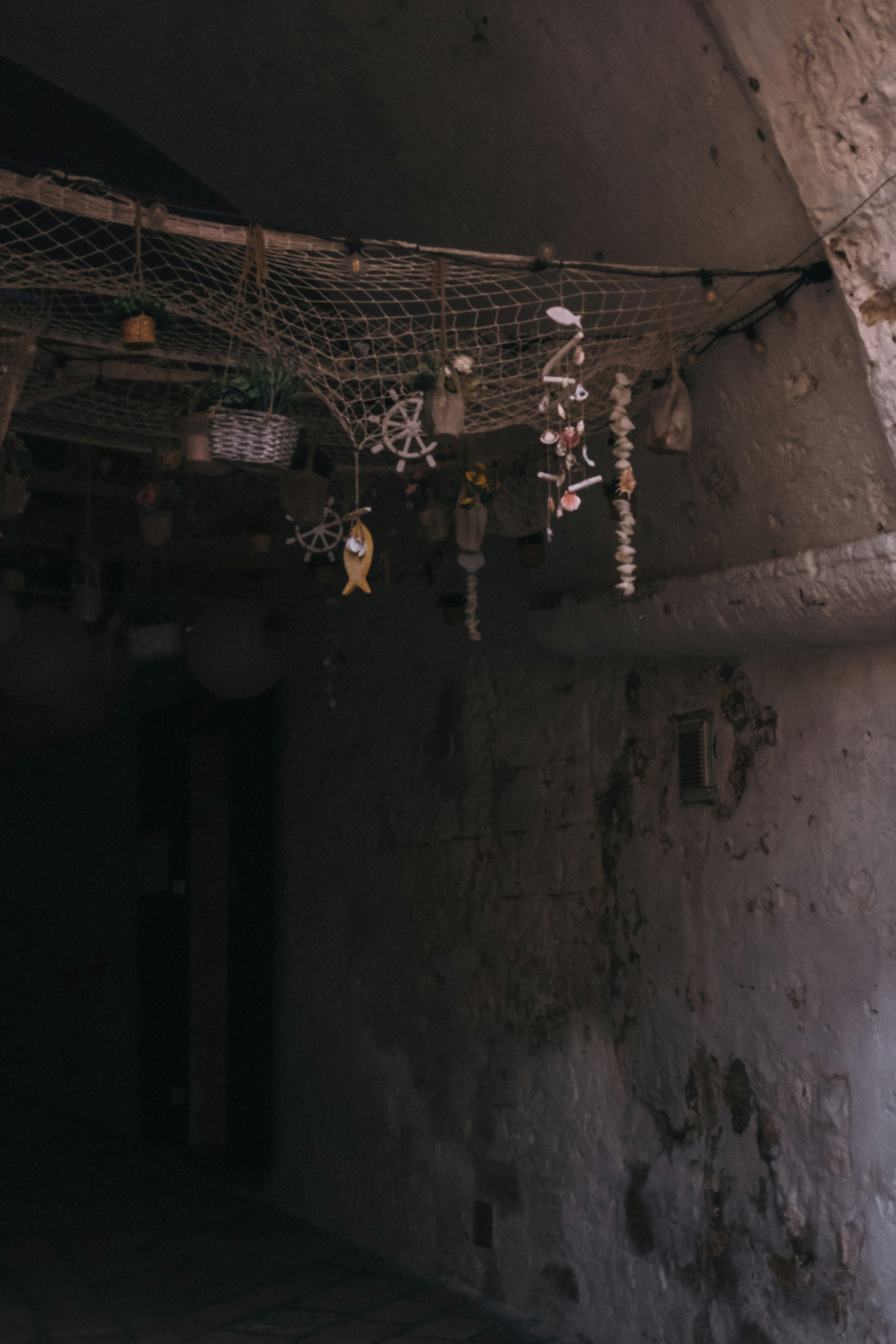 Decorative netting adorned with seashells and nautical elements hangs from the ceiling of a rustic hallway, evoking a seaside charm.