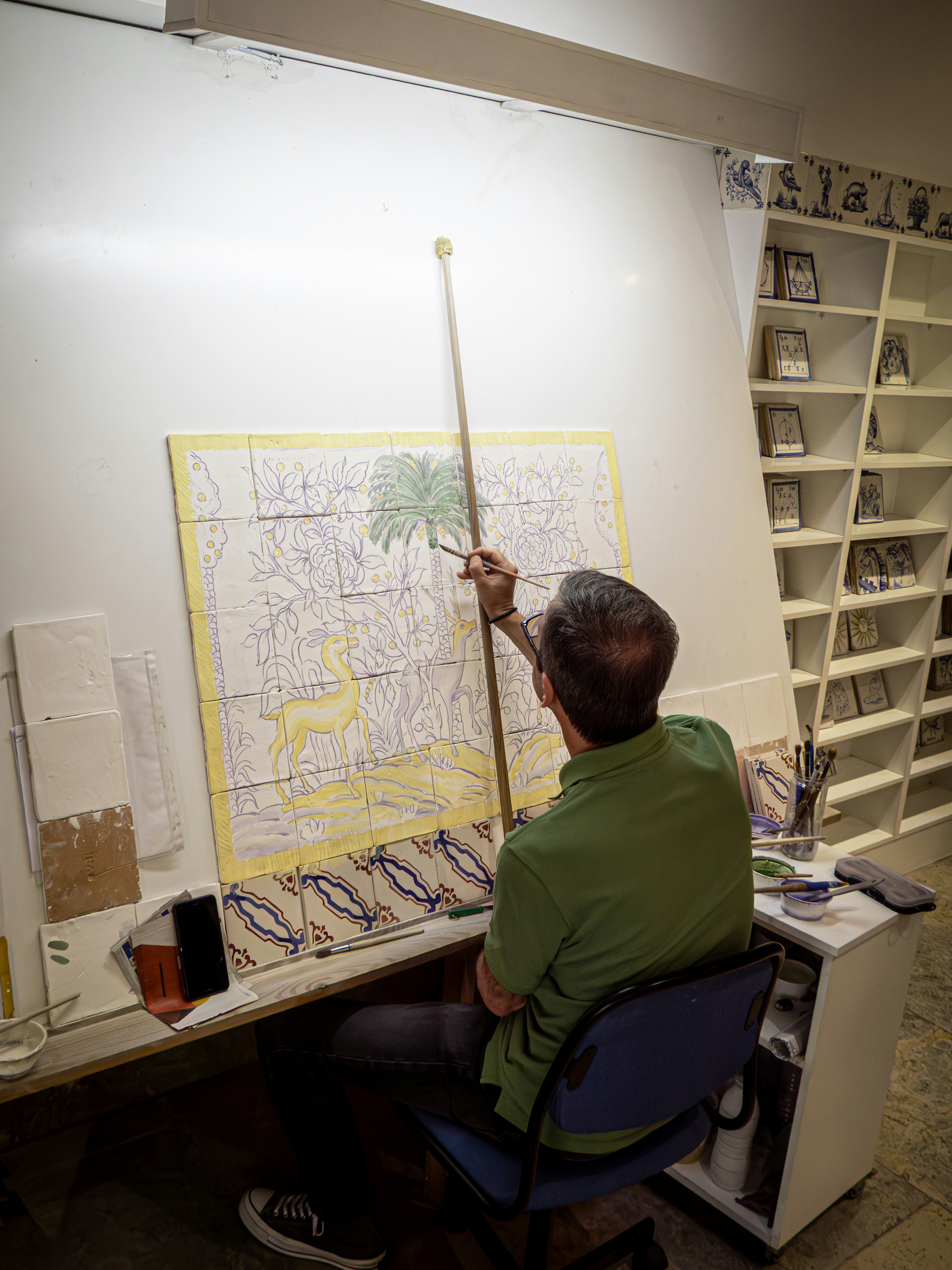 In a quiet workshop in Lisbon, a craftsman breathes life into traditional azulejos — Portugal’s iconic hand-painted ceramic tiles. Every stroke of the brush connects centuries of cultural heritage with the present moment. This image captures a fleeting pause in the artist’s patient work, a tribute to manual skill in an increasingly digital world. | An artist paints a mural on a large white board.