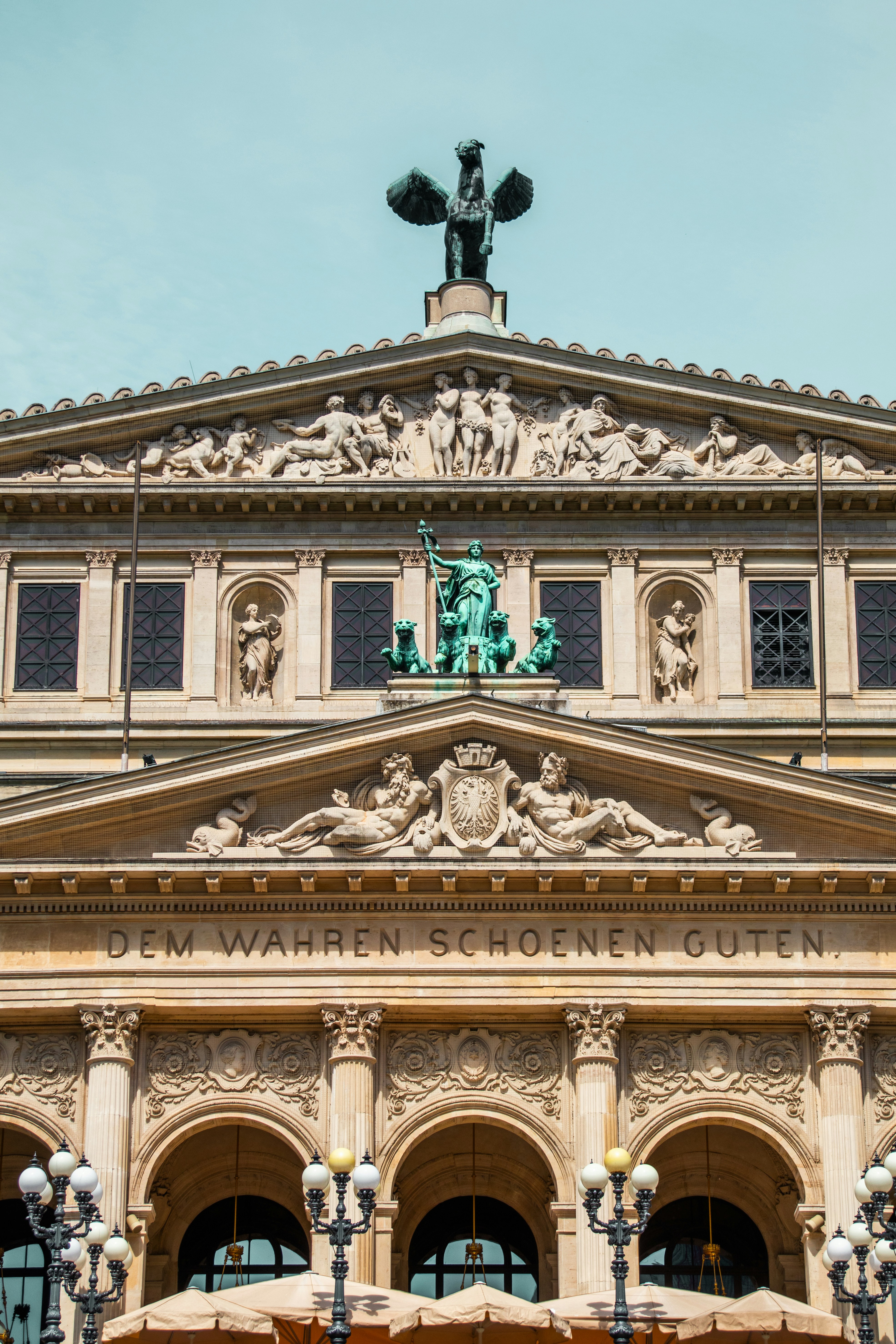 Ornate building facade featuring intricate sculptures and a prominent statue, with the phrase 'DEM WAHREN SCHOENEN GUTEN' elegantly displayed.