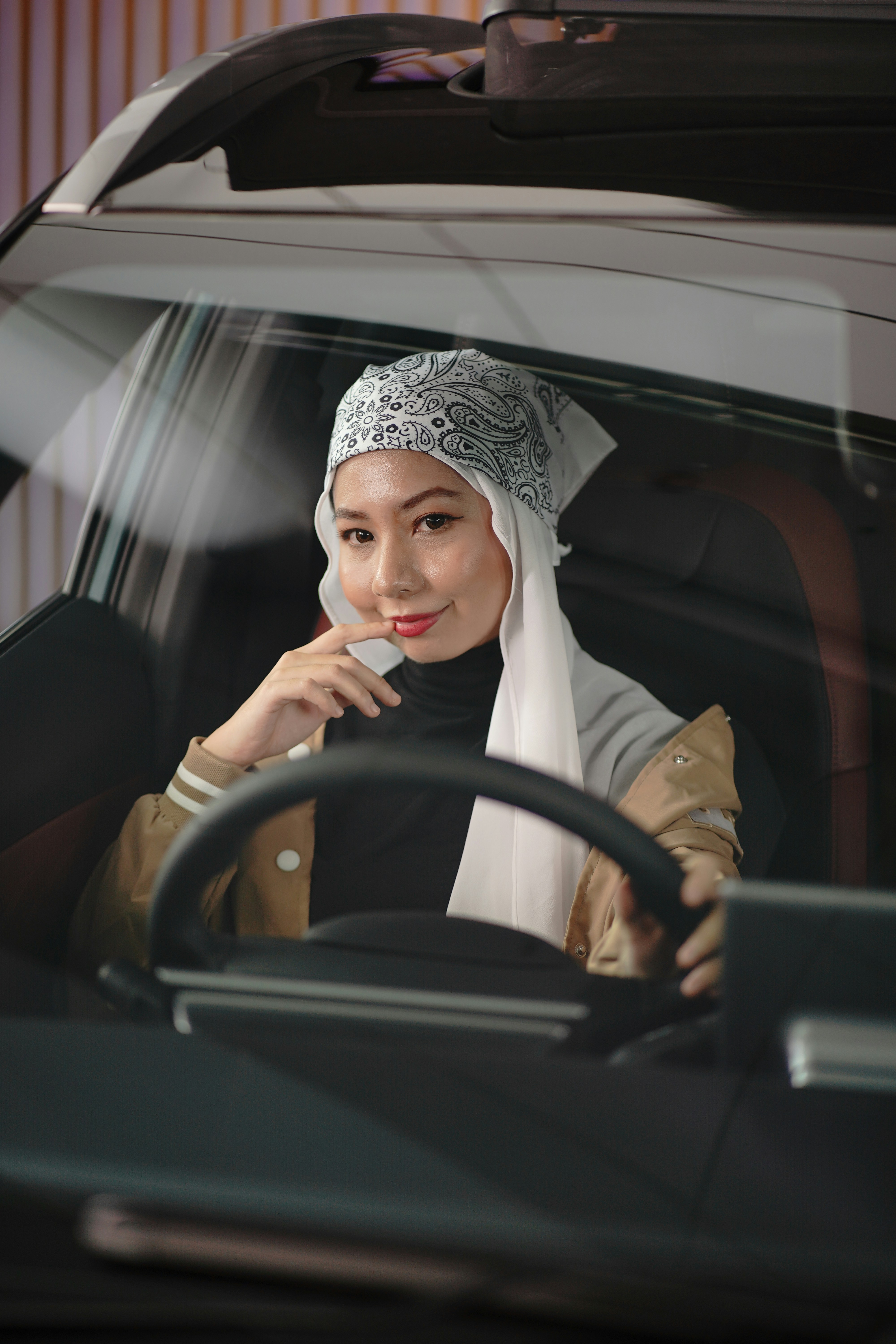 Young woman with a stylish headscarf seated in a car, exuding confidence and poise. The interior reflects a contemporary design aesthetic.