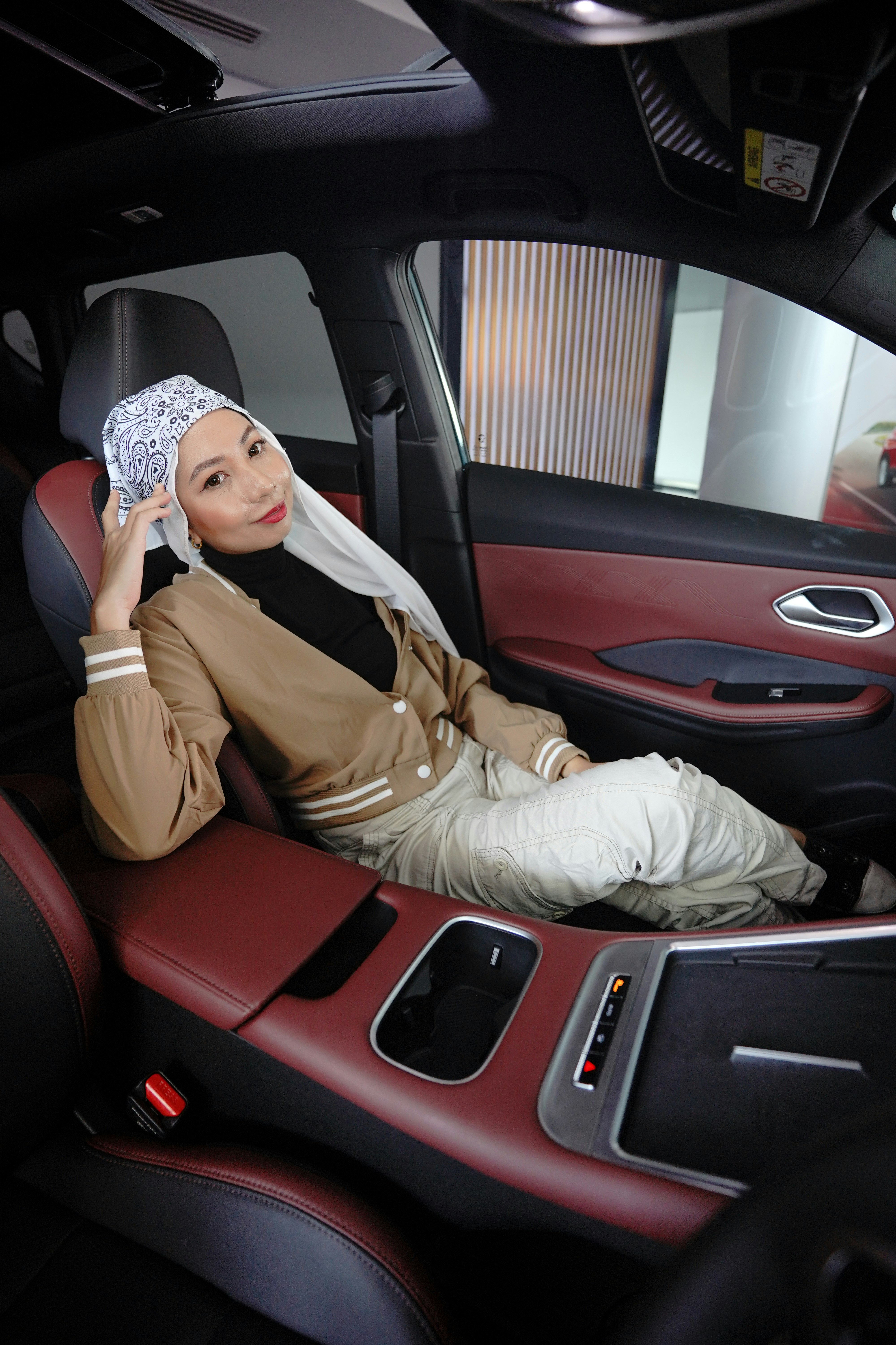 A stylish individual relaxes in a luxury car interior, showcasing a blend of contemporary design and comfort. The rich colors and textures of the cabin enhance the overall aesthetic.