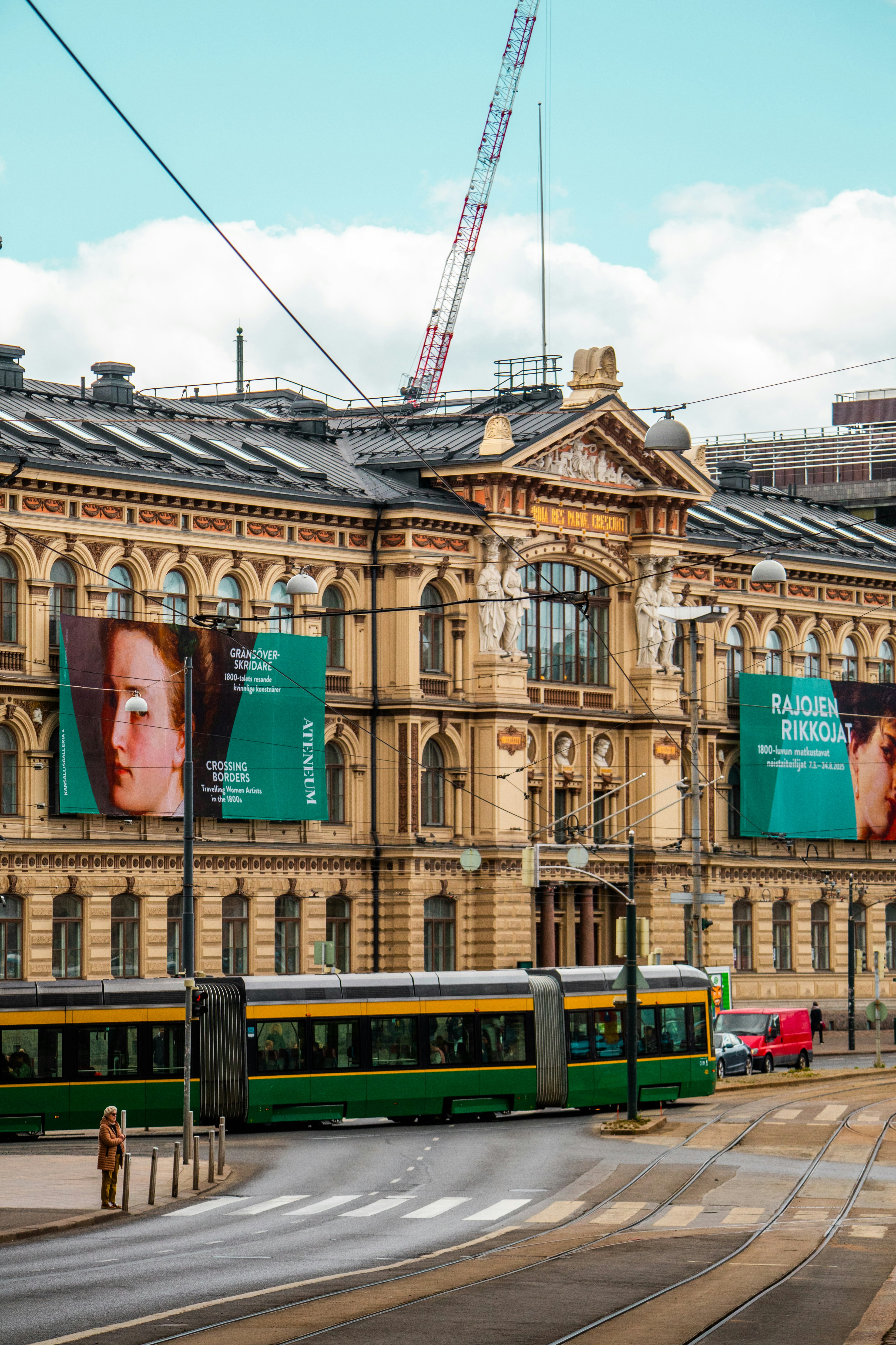 Historic building adorned with large advertisements, showcasing a blend of modern art and classic architecture. A green tram passes in the foreground.
