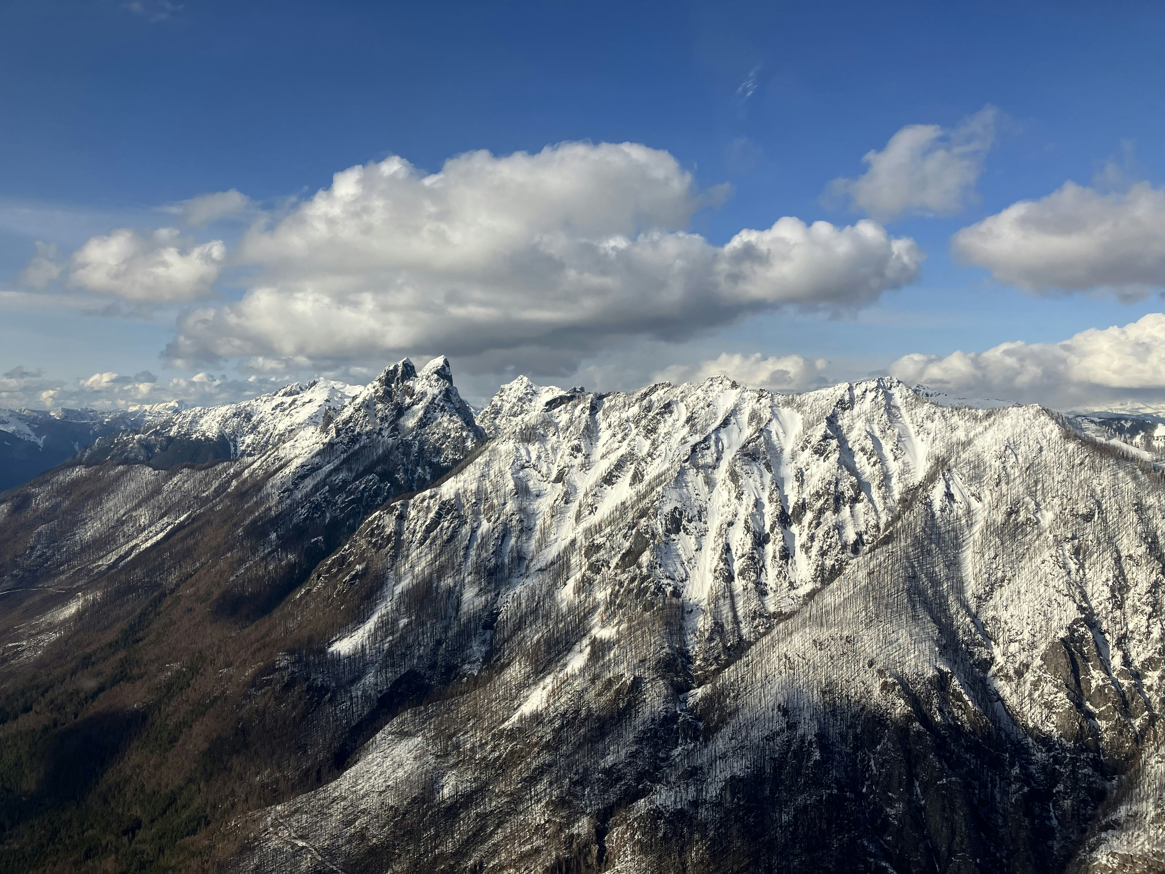 Snow capped peaks of the | Snow-capped mountains rise beneath a cloudy blue sky.