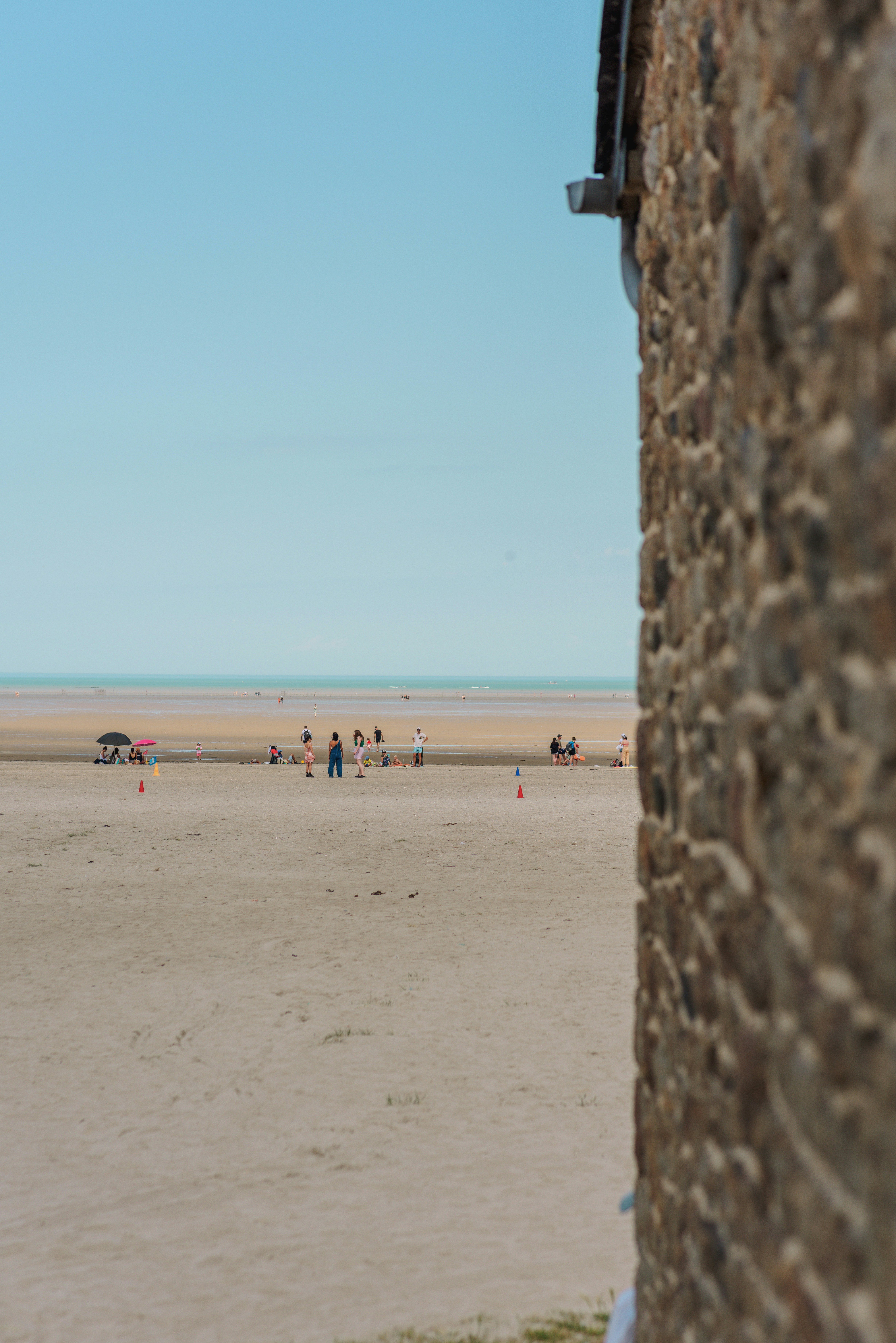 Beachgoers enjoy a sunny day near a stone building.
