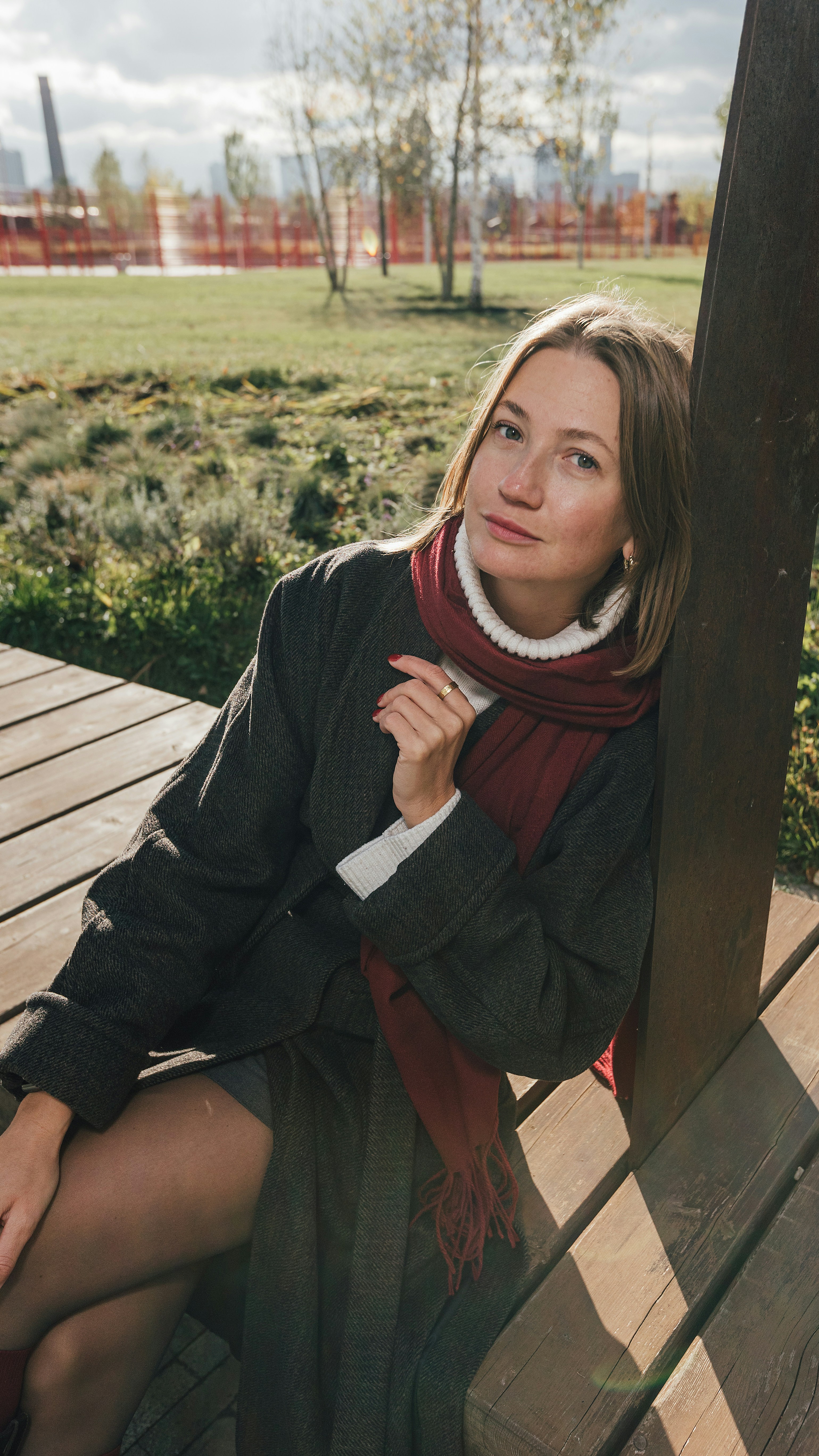 Woman sitting outdoors wearing a scarf and coat.