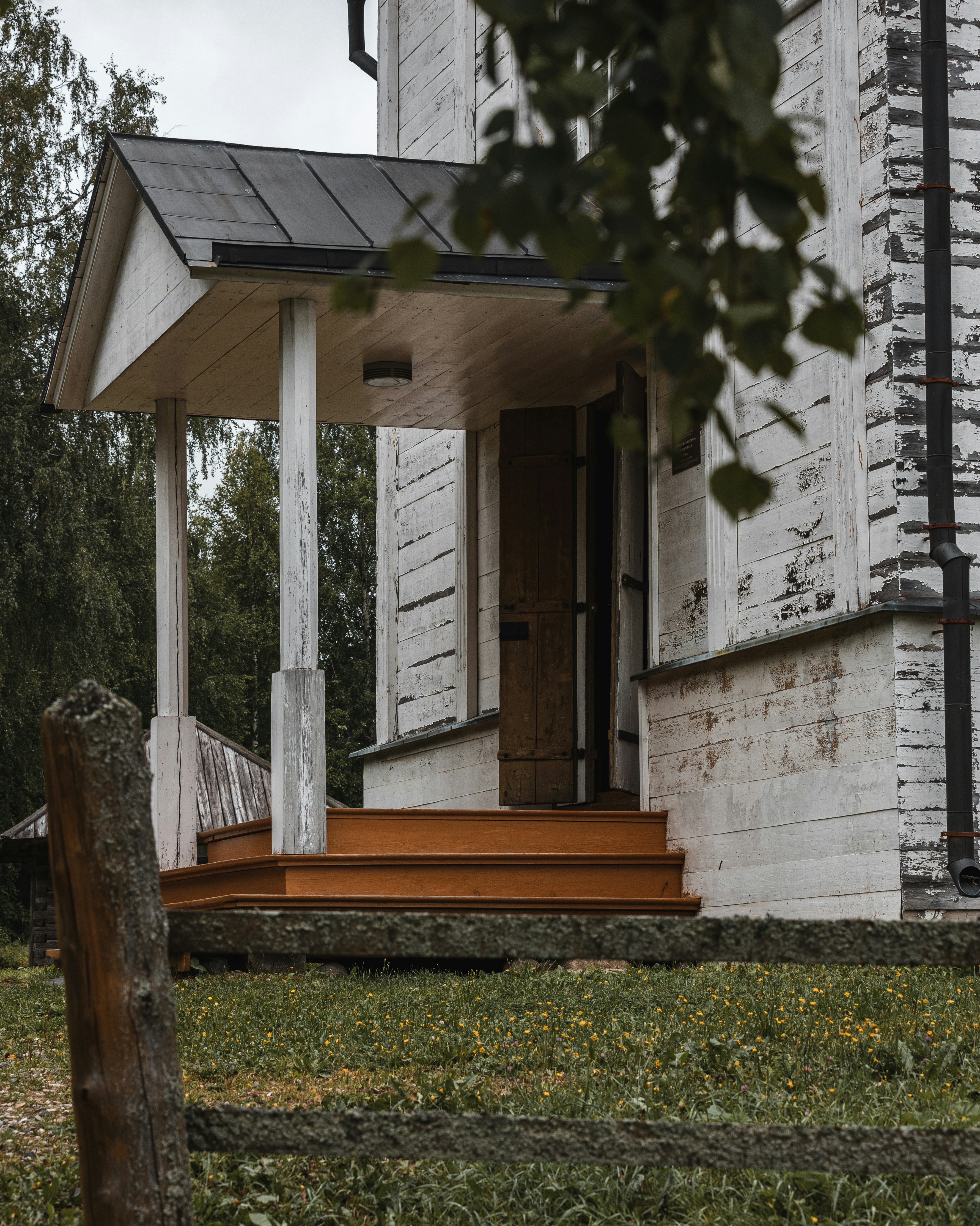 Elegant wooden house with a distinct orange staircase, surrounded by lush greenery and rustic fencing.